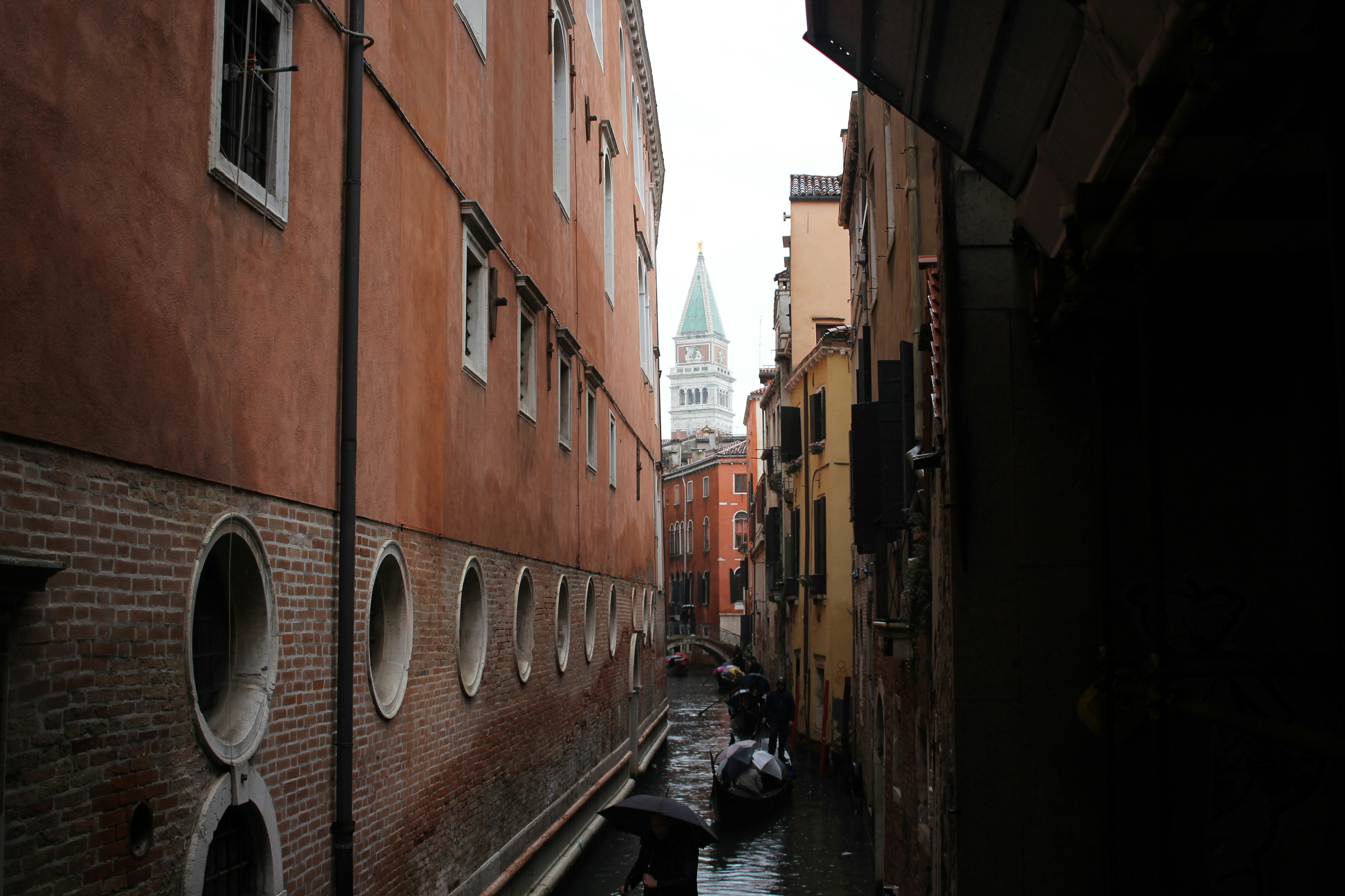 A narrow canal running between two buildings with a clock tower in the ...