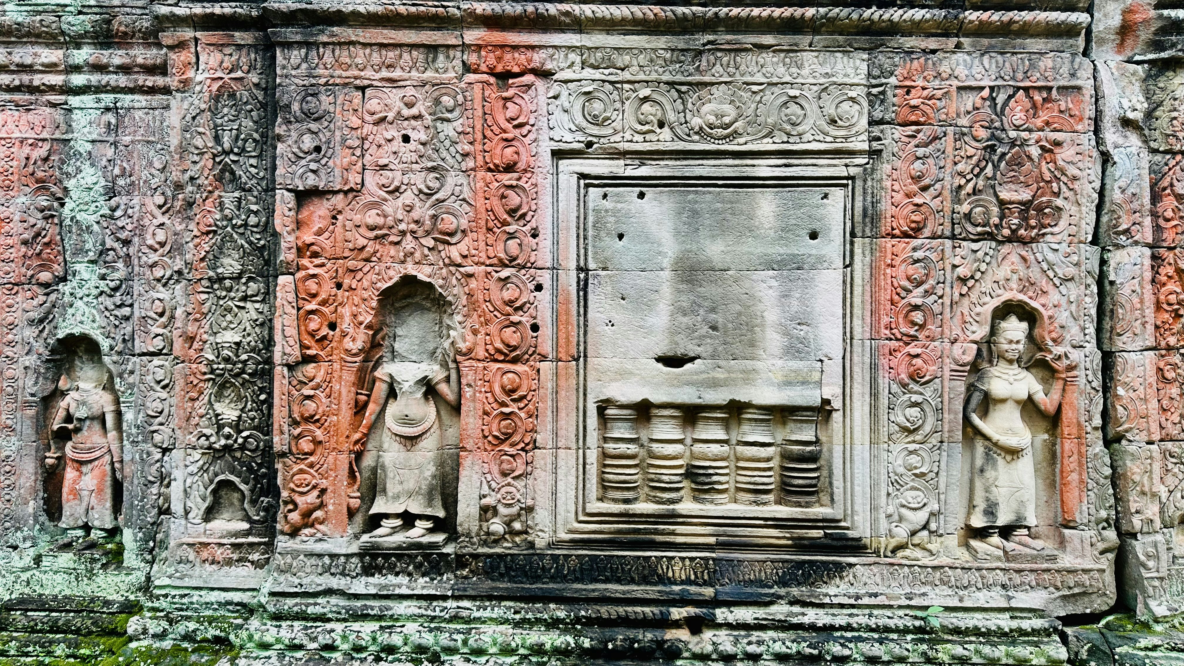 Three Stone Guardians Framing a Weathered Central Panel on a Moss-Covered Temple Frieze