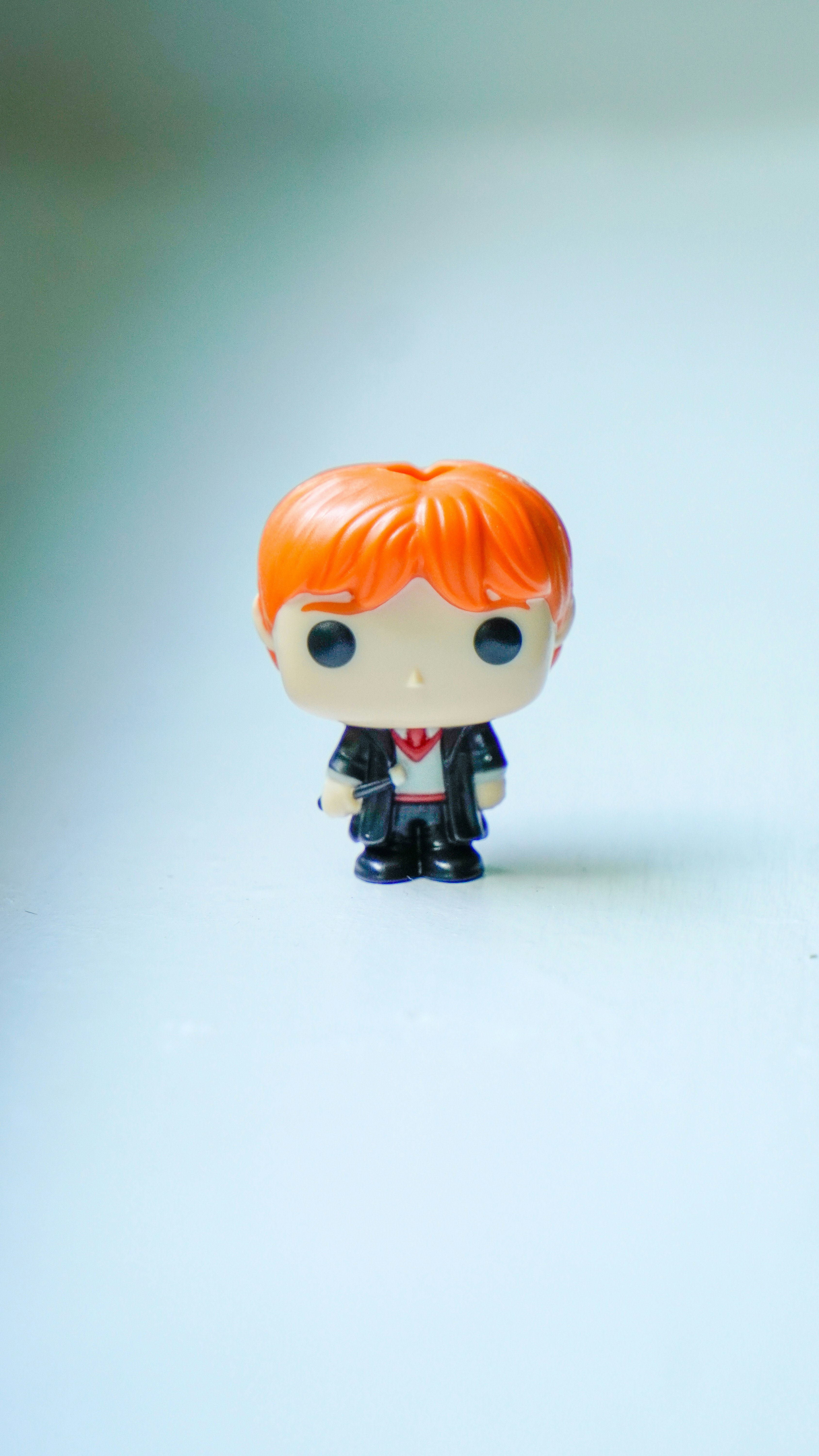 Small vinyl figure with orange hair stands on a smooth, light blue surface.