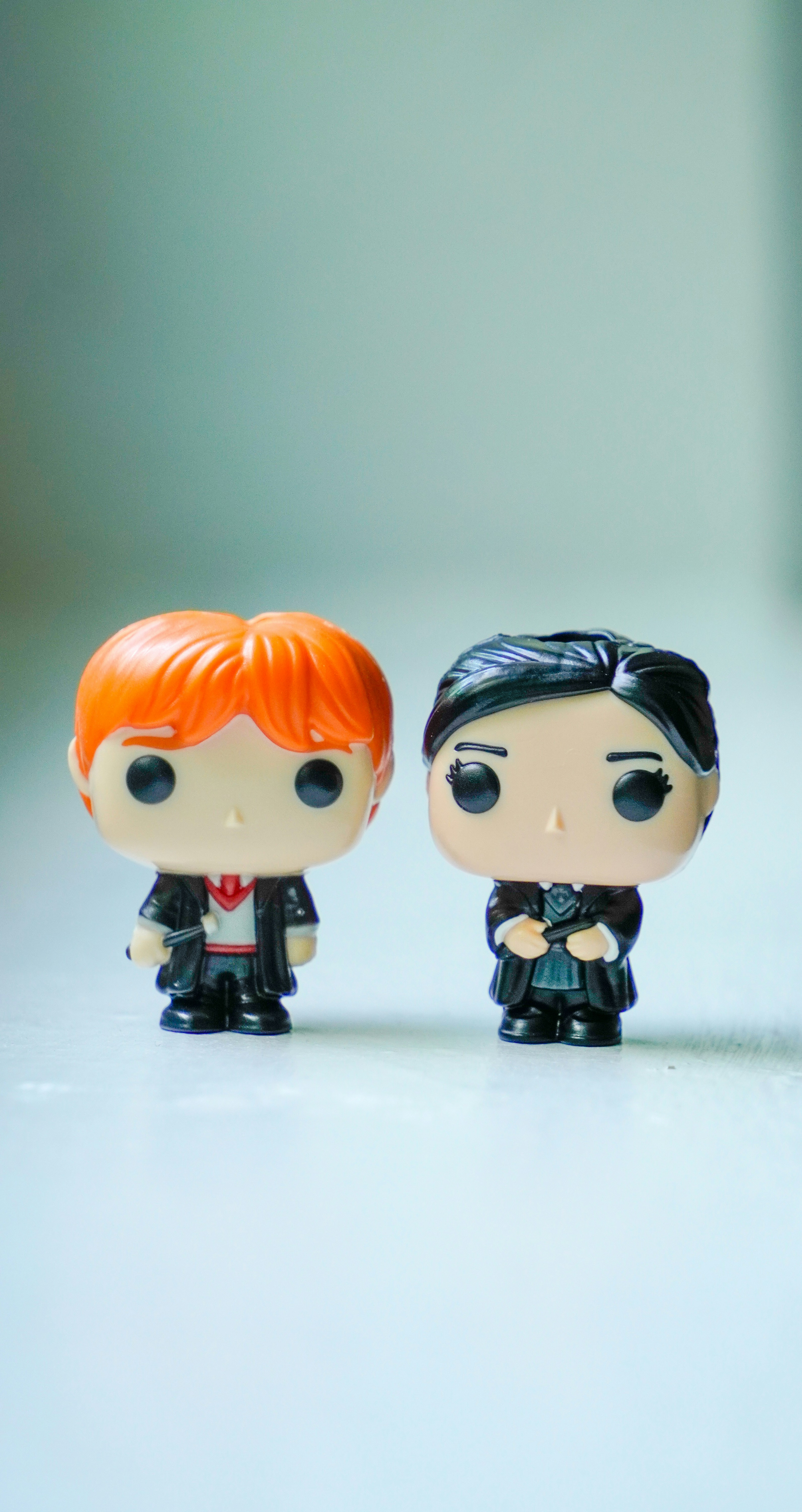 Two Tiny Vinyl Figures Stand Side by Side on a Pale, Blur-Washed Surface