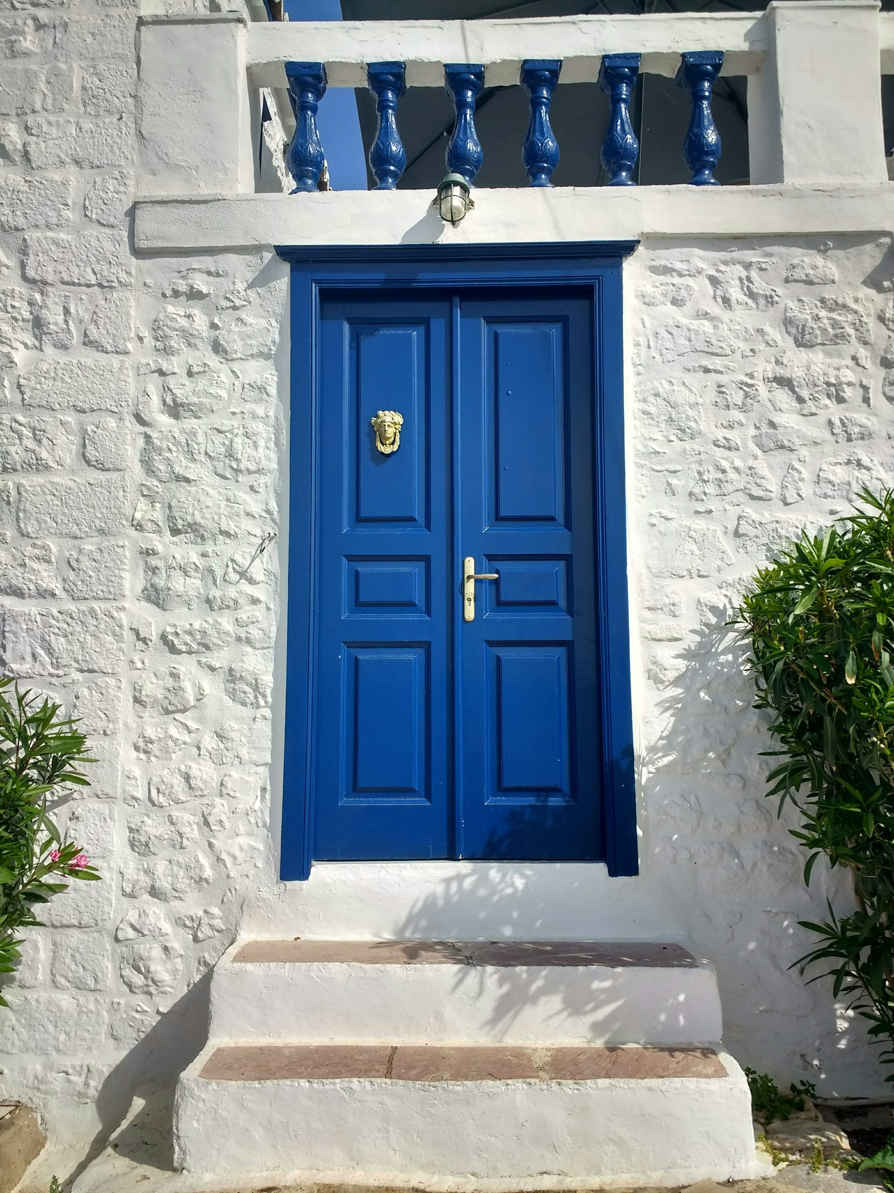 Vibrant blue door framed by white stone walls and lush greenery, inviting exploration. The door features a decorative knocker, enhancing its charm.