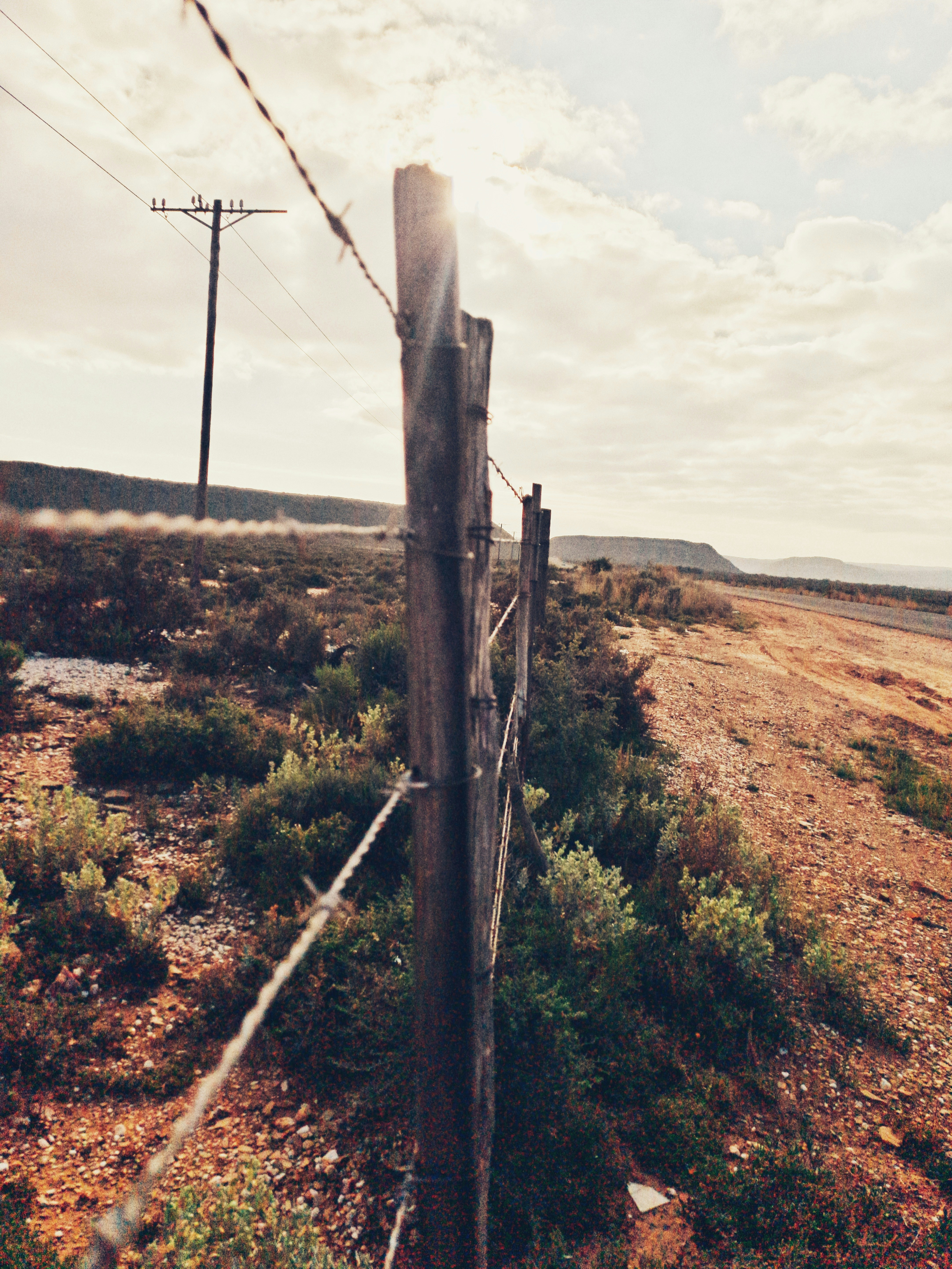 Fence post on the side of the road | A wooden fence sitting next to a dirt road