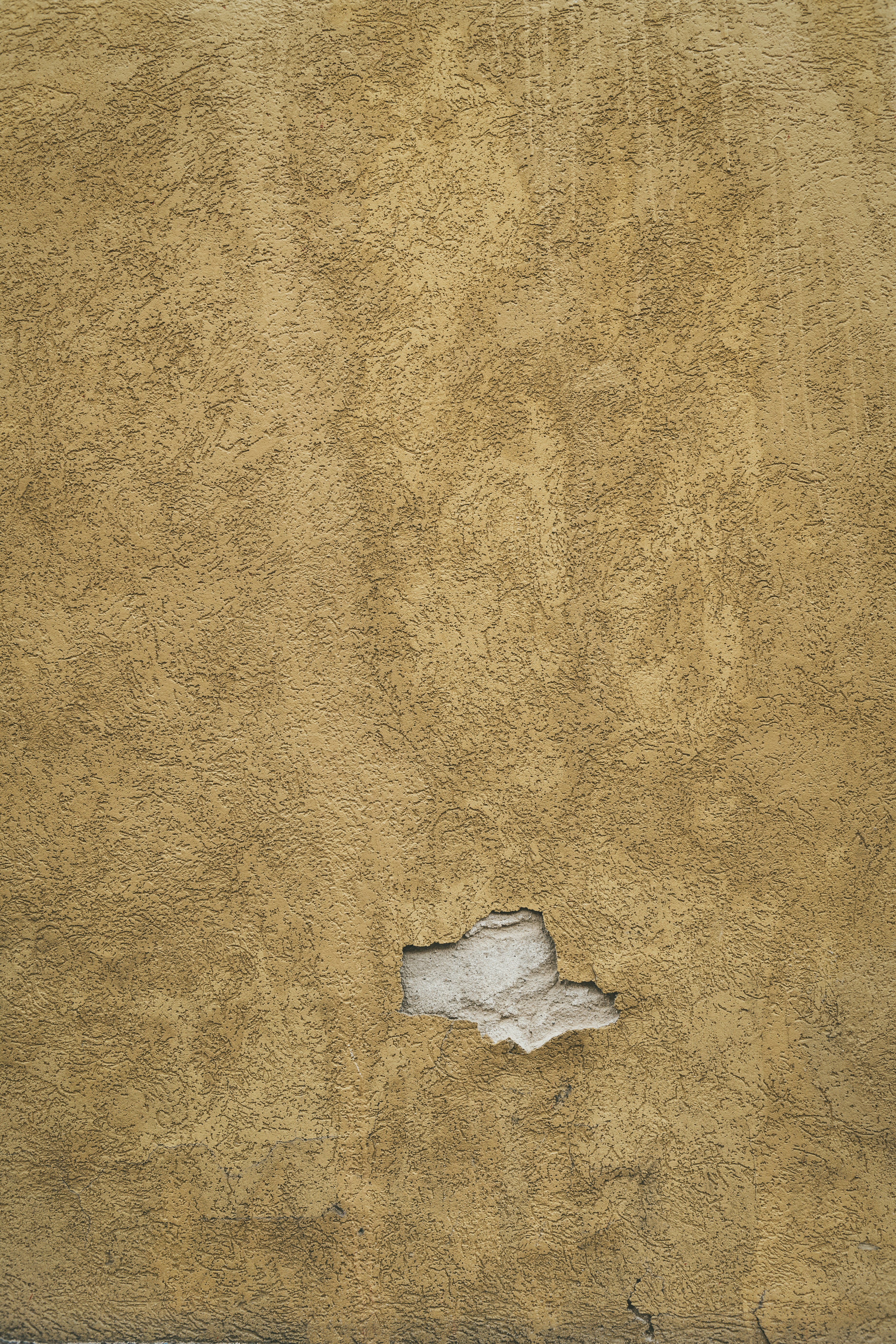 Weathered yellow wall with a patch of exposed white beneath.