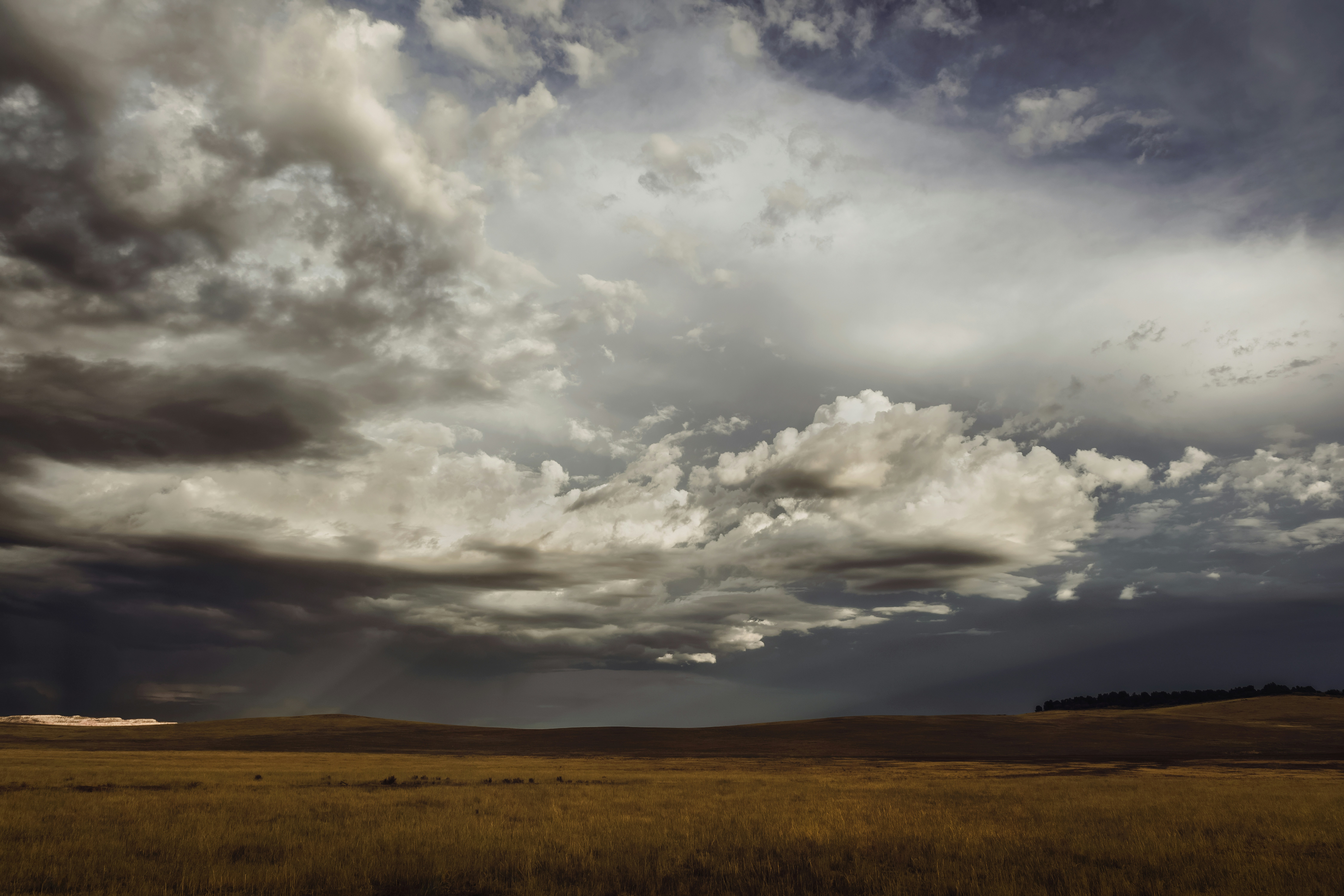 Expansive plains under dramatic, swirling clouds with hints of sunlight breaking through.