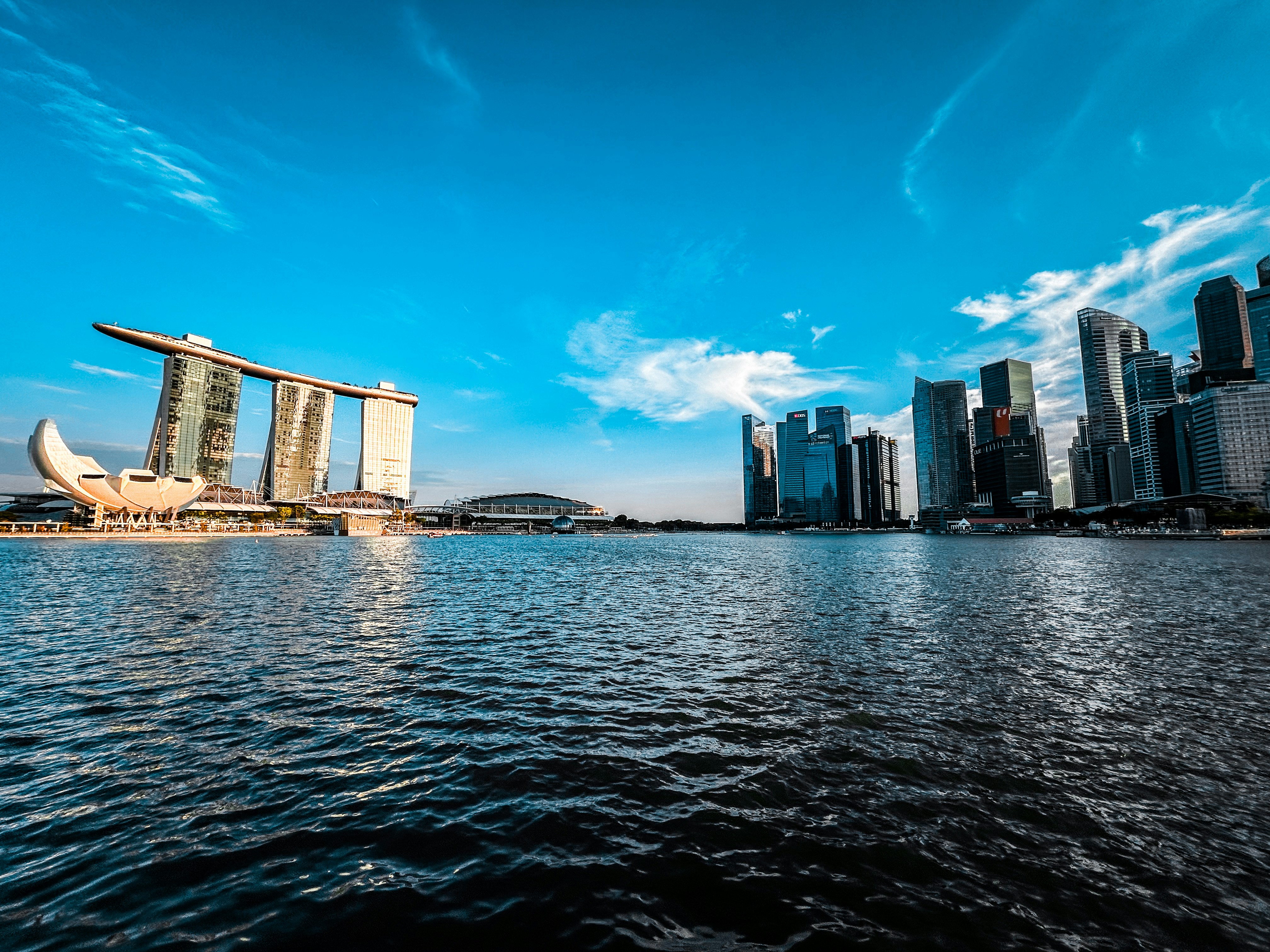 Modern skyline of Singapore reflecting on calm waters under a vibrant blue sky.