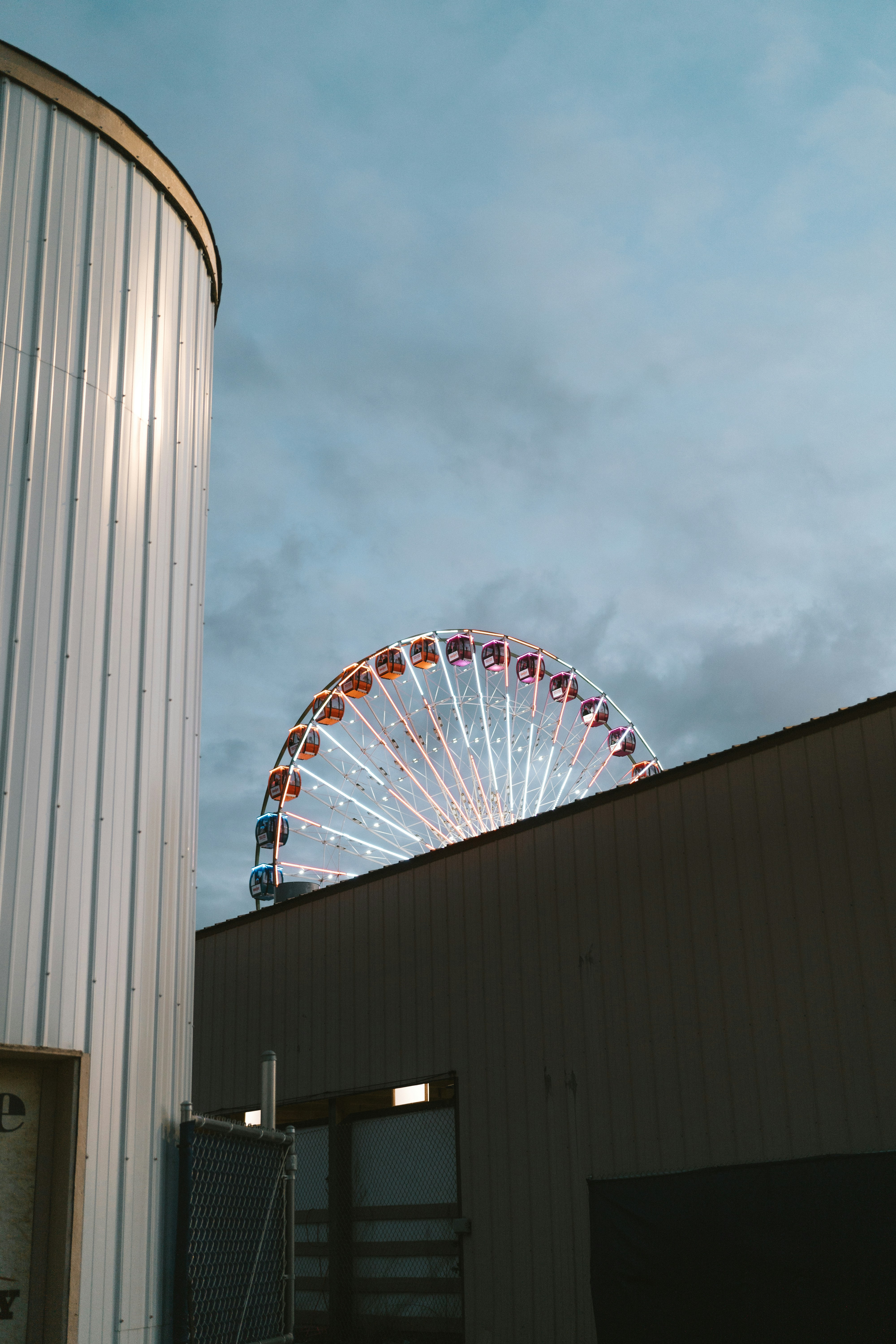 Pastel Ferris Wheel Peeking Over Industrial Rooflines