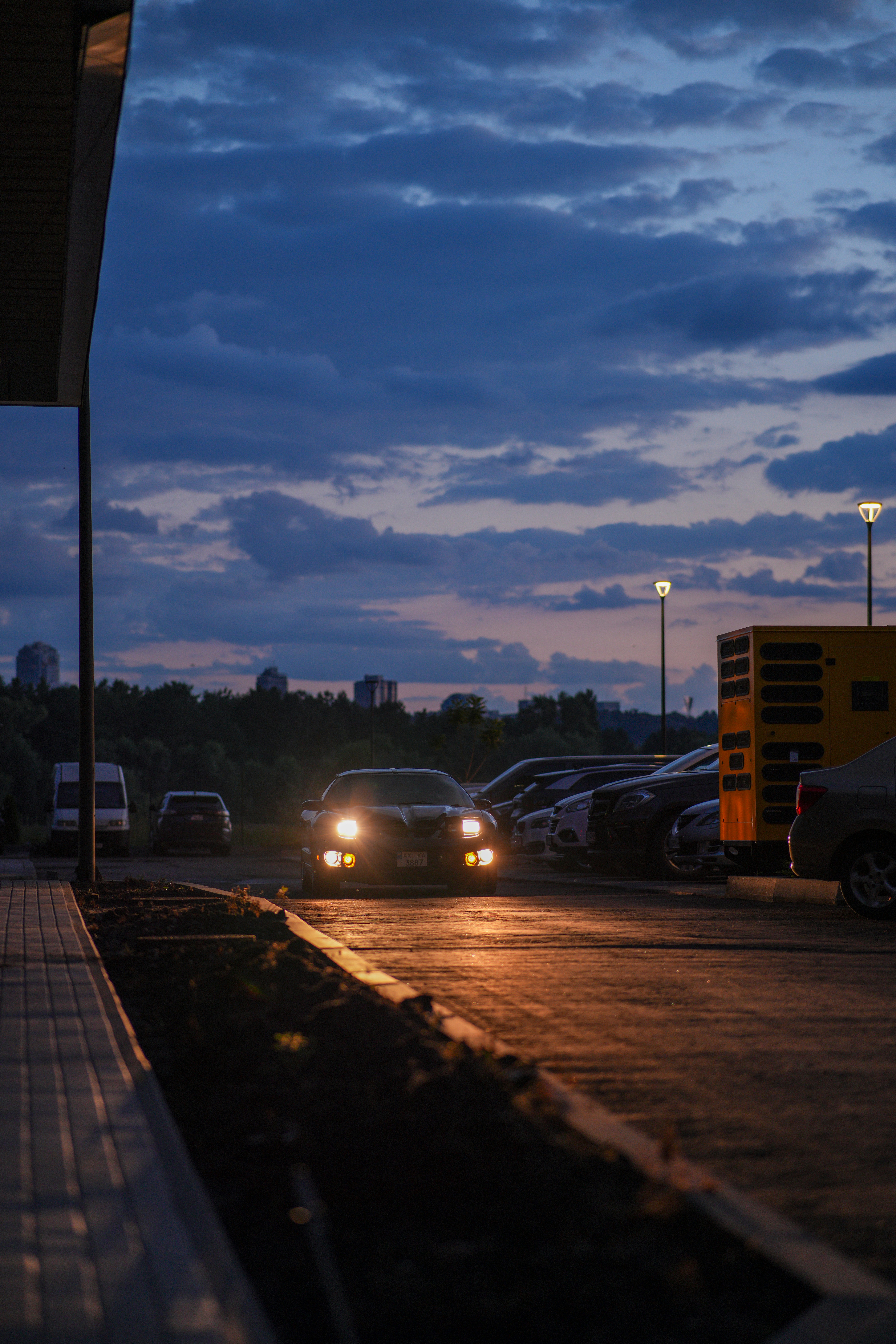 Dusk Approach: Headlights Cutting Through a Quiet Parking Lot