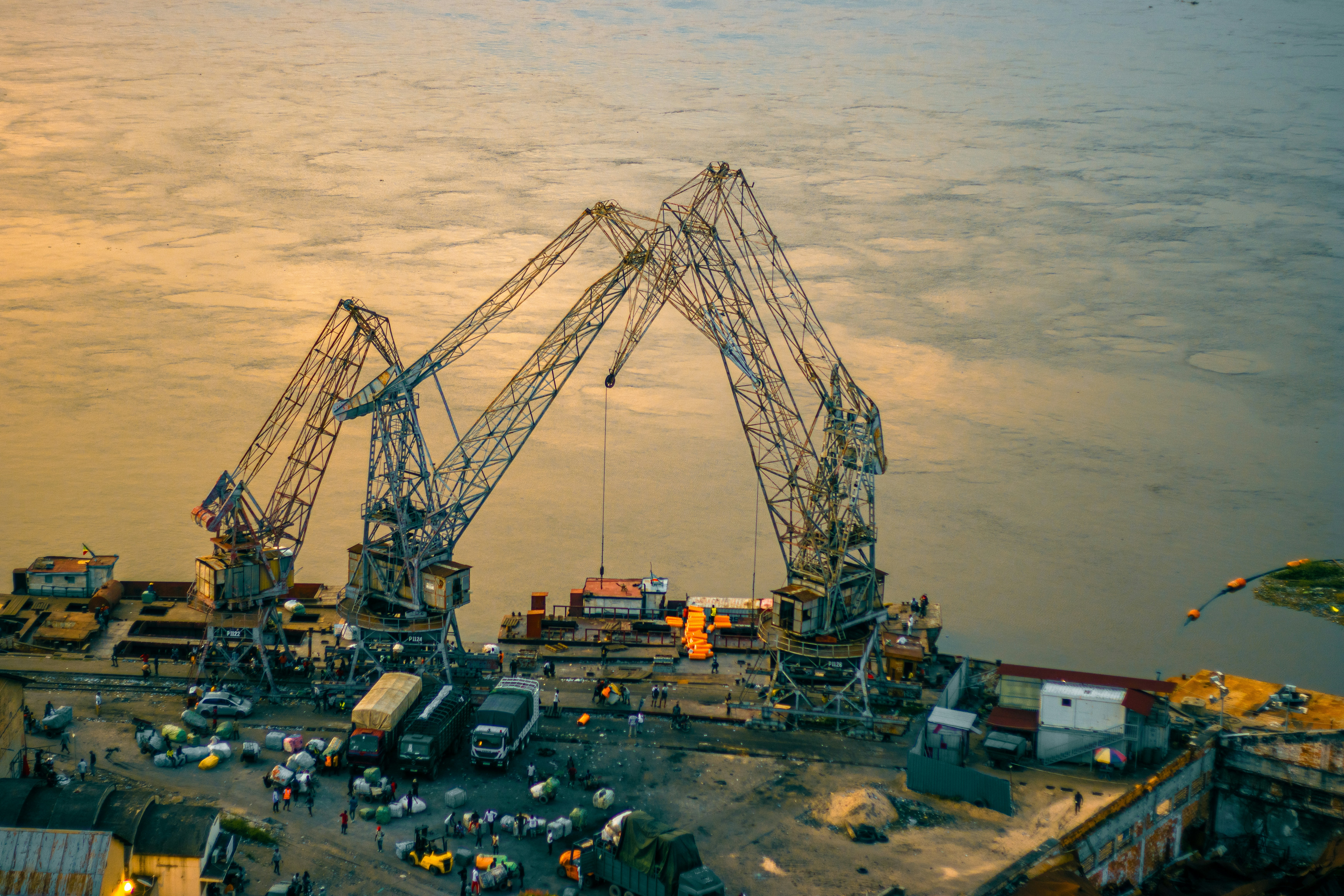 Two towering cranes poised over a river at sunset, casting reflections on the water.