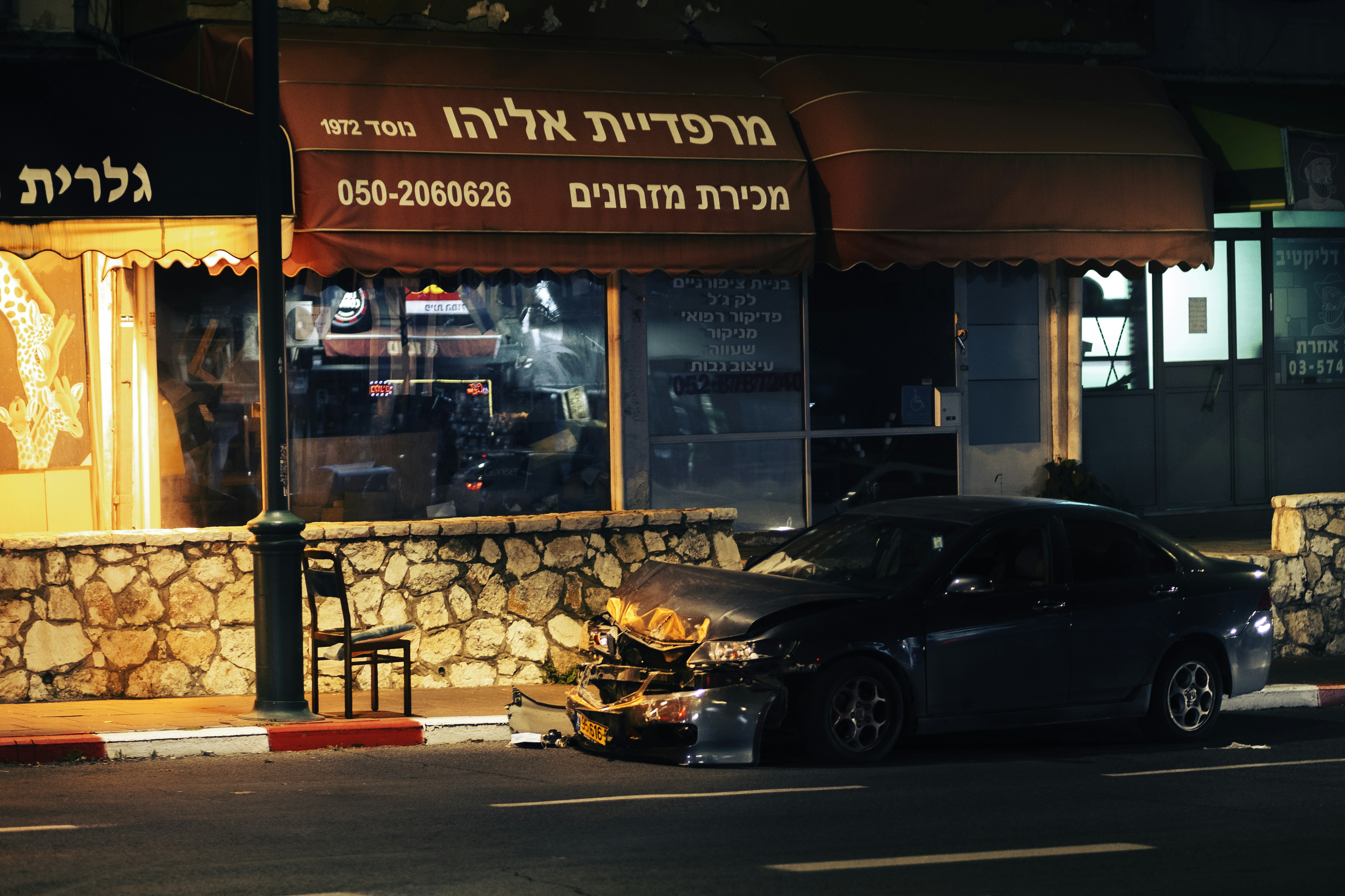 Nighttime Street Scene: A Stricken Car Under Neon City Awnings