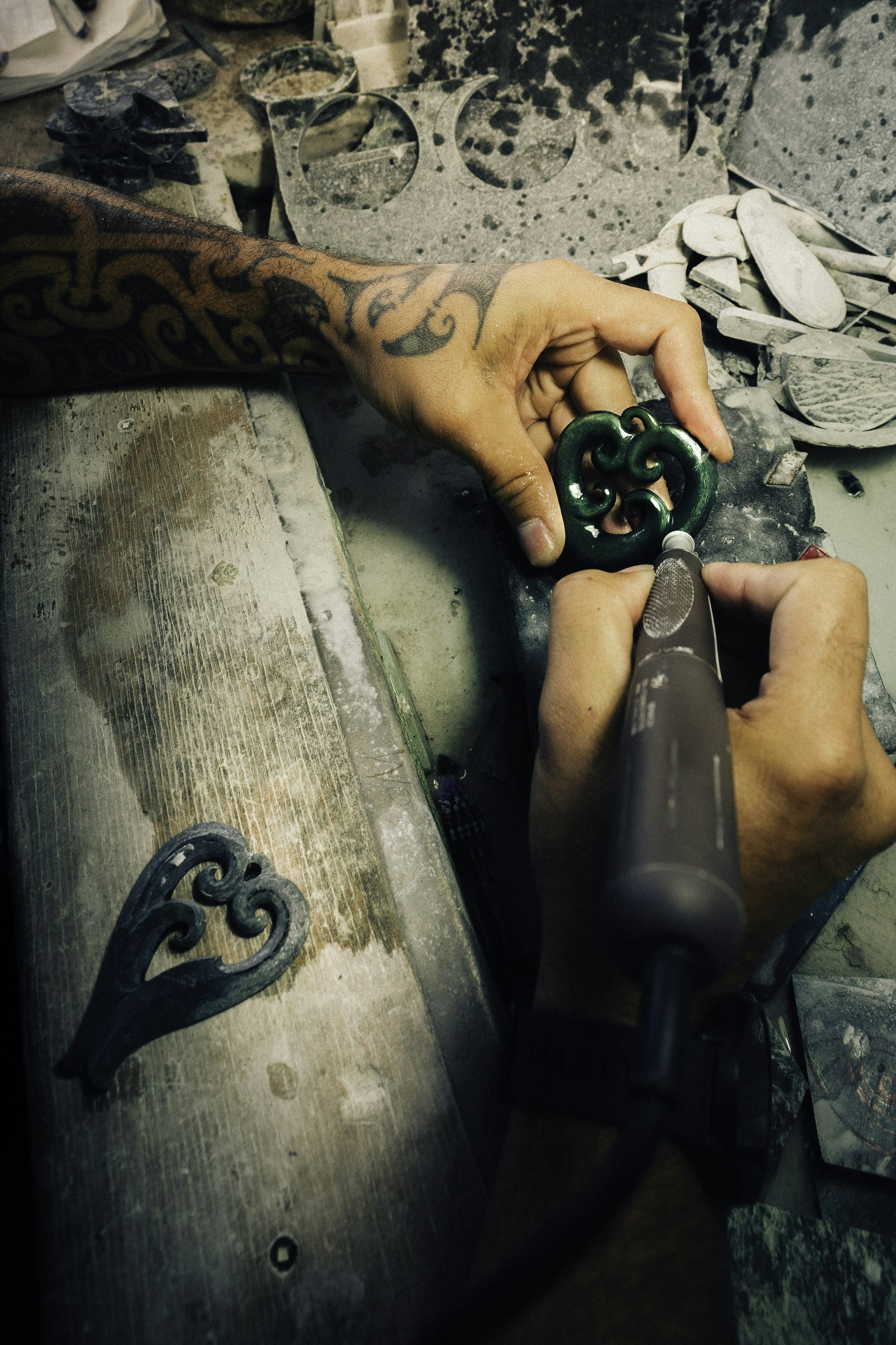 Green Orbit Pendant: Tattooed Hands Carving a Circular Ornament in a Dusty Studio