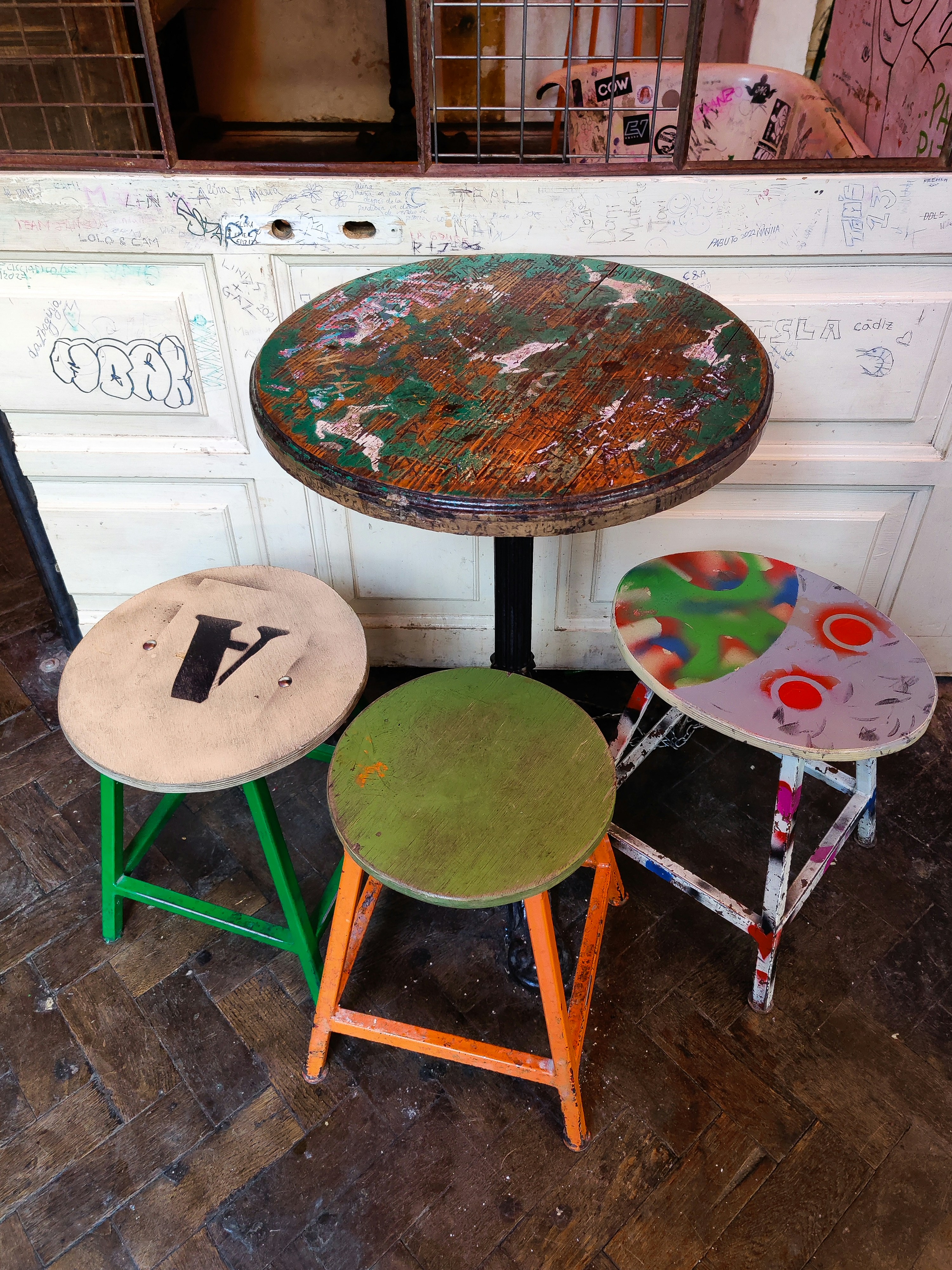 Weathered Circular Table Surrounded by a Colorful Stool Quartet in a Graffiti Café Nook