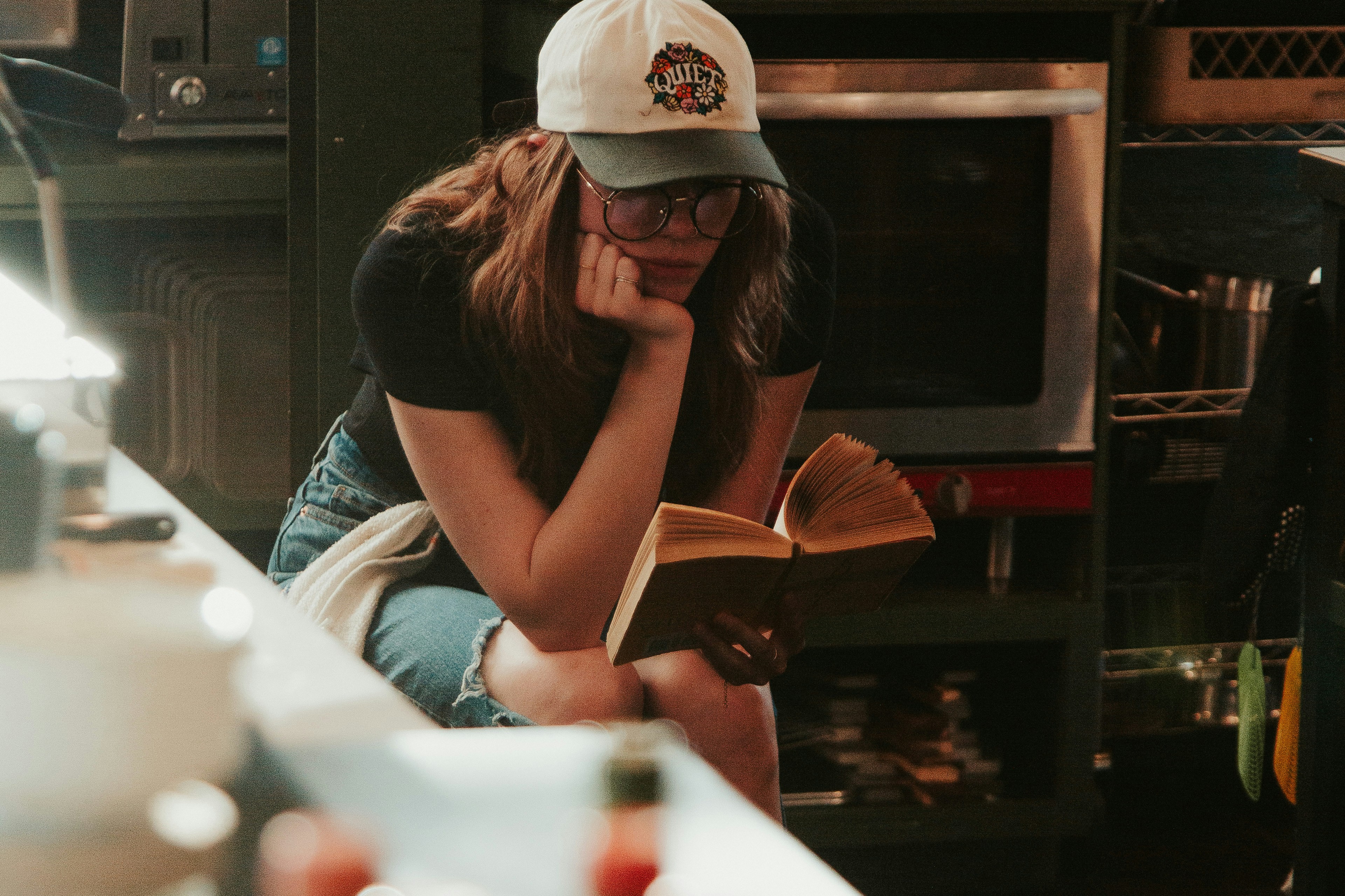 Reading in the Kitchen Light: A Quiet Moment with a Cap and Glasses