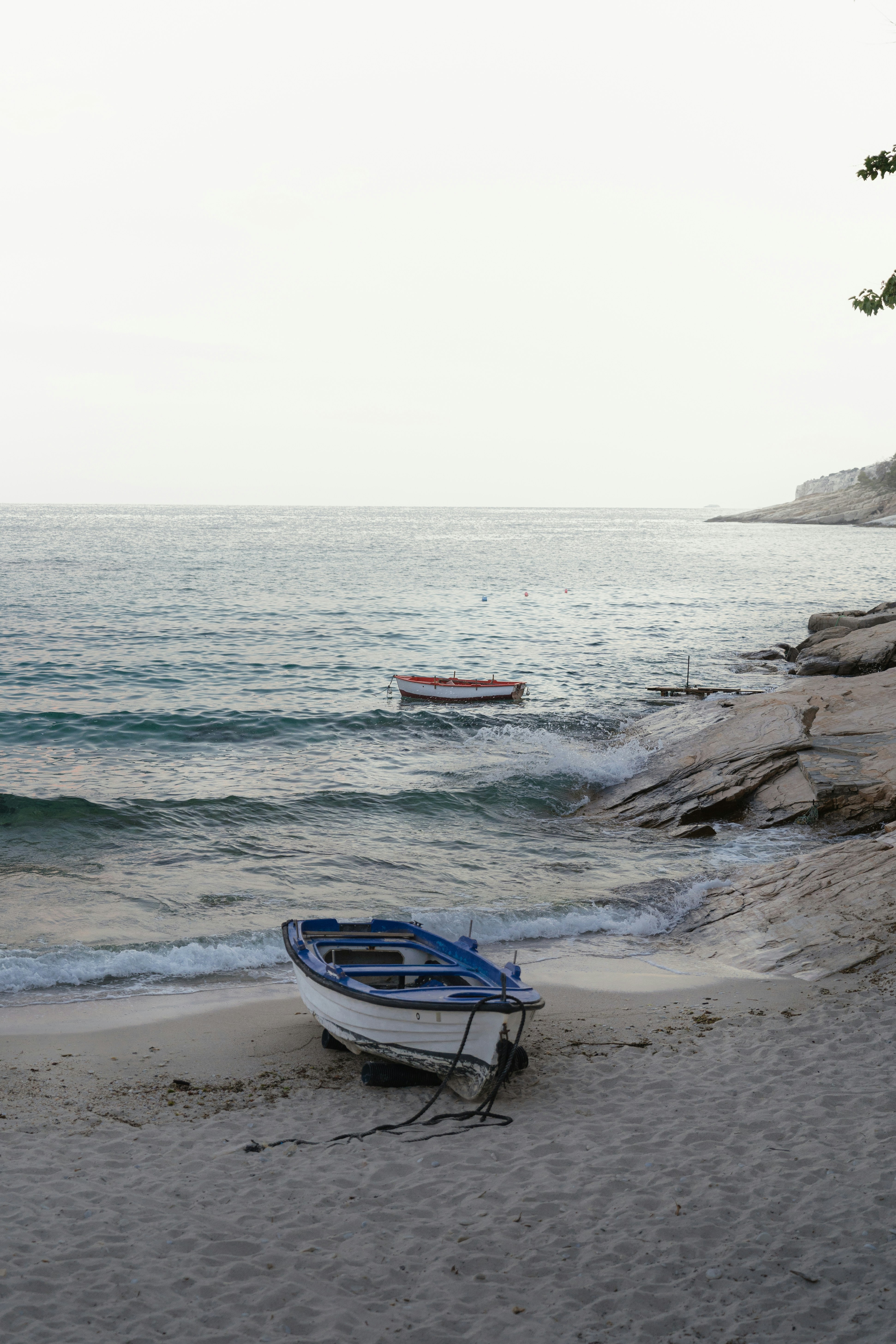 Blue-Trim Boat Resting on Quiet Sand by a Granite Shore