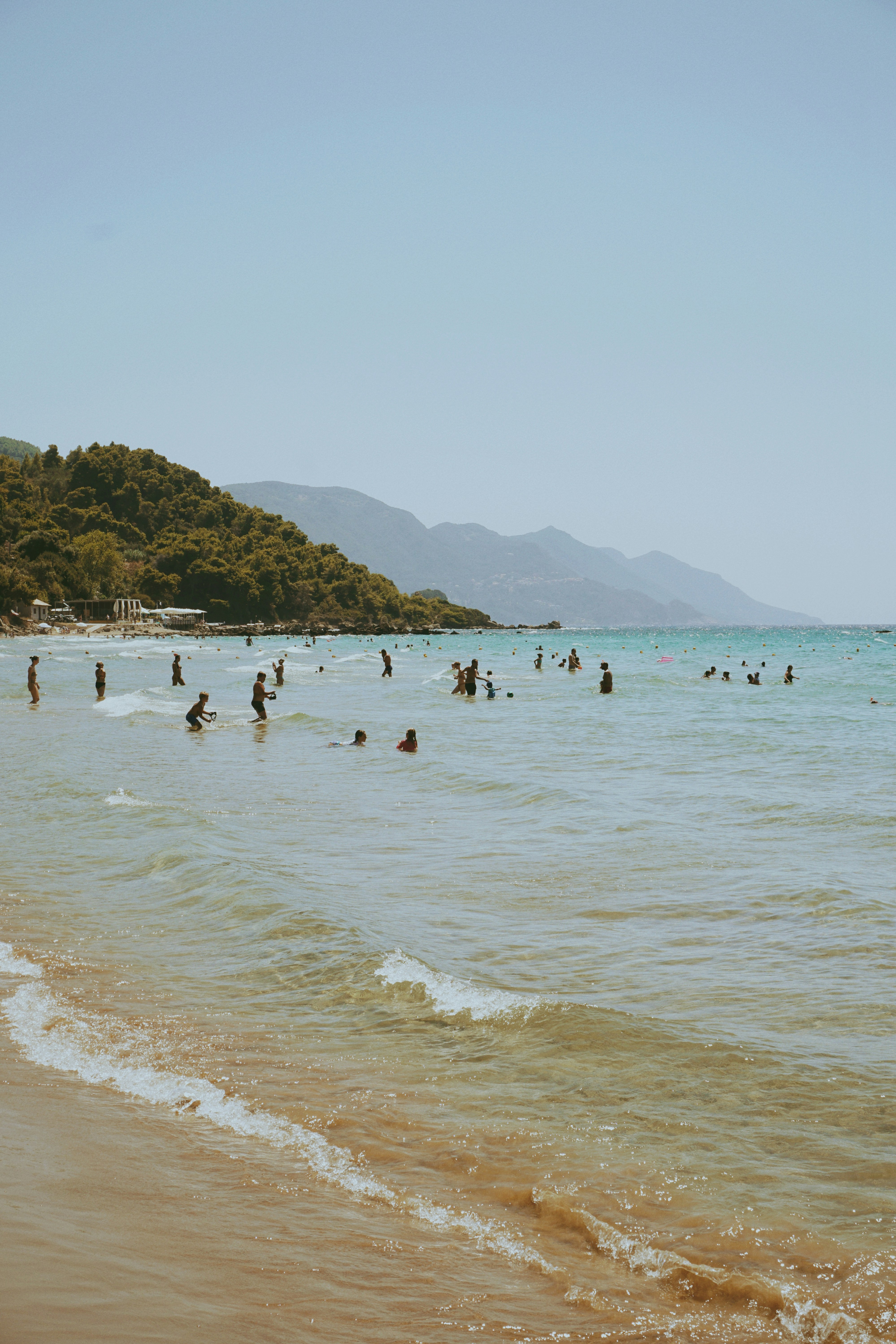 Turquoise Tide at the Headland: A Busy Beach Beneath a Quiet Mountain Backdrop