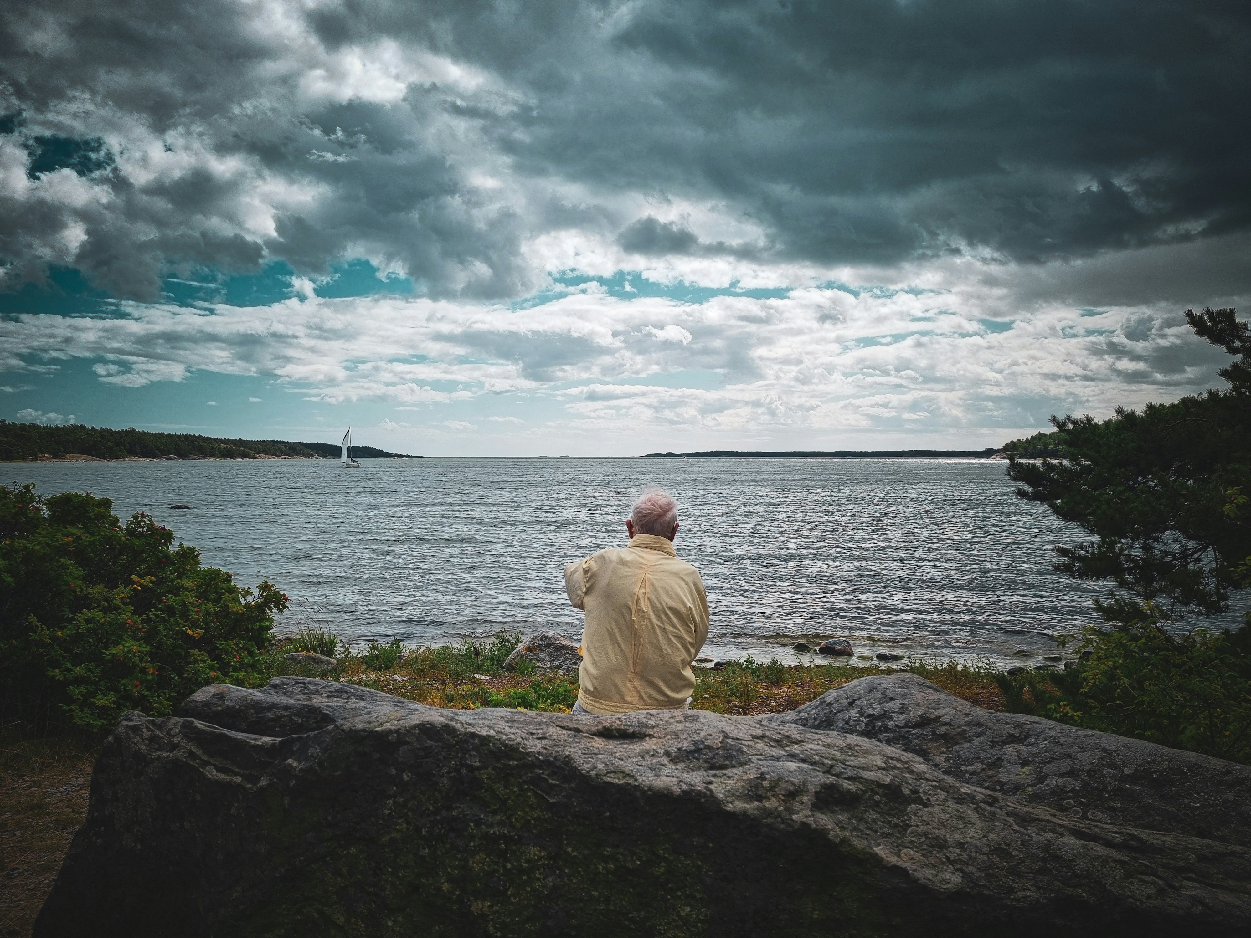 Person seated on a rock gazing at a vast, cloudy seascape.