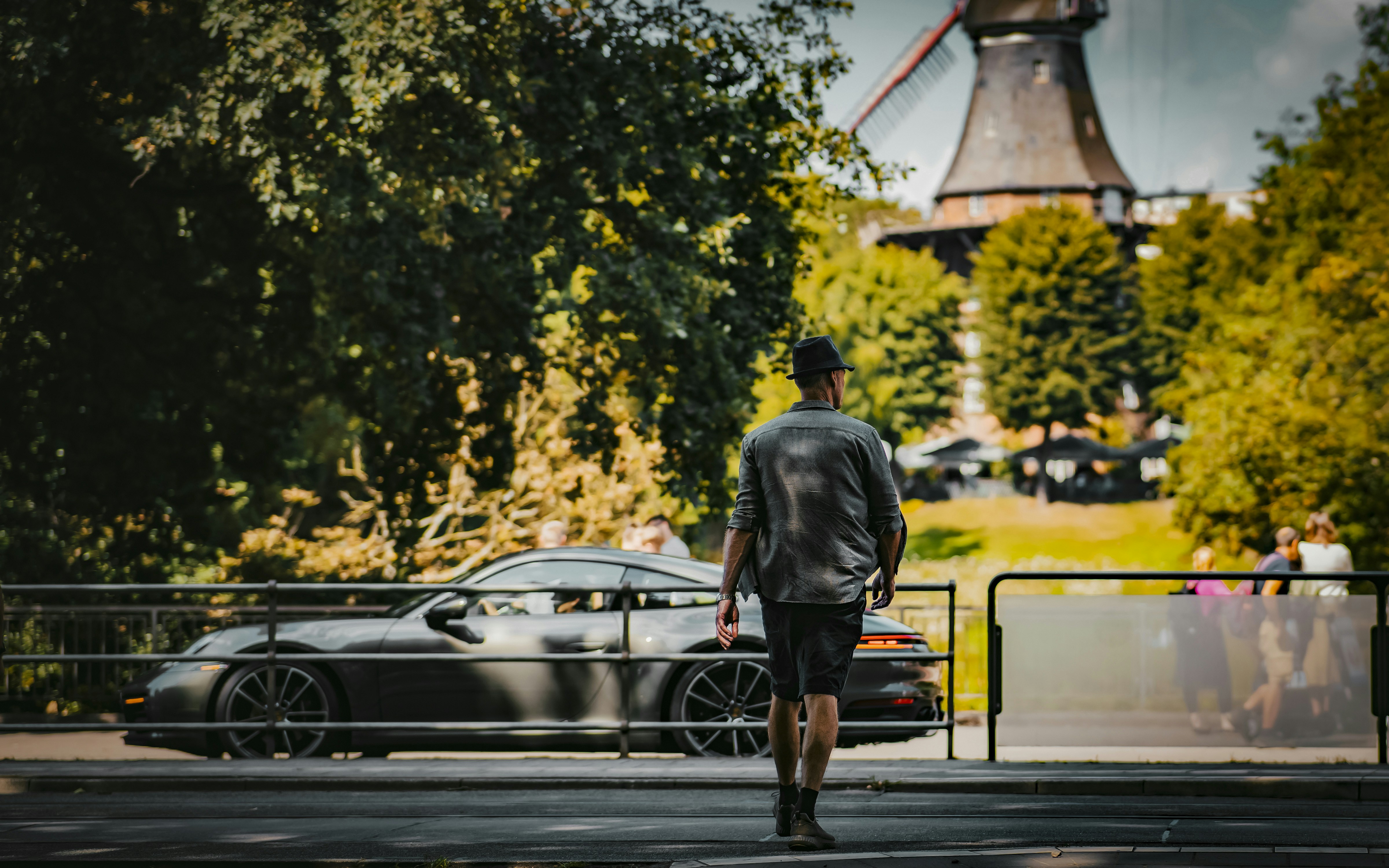 Stride Toward the Windmill: A leather-clad figure beside a sleek car in a sunlit plaza