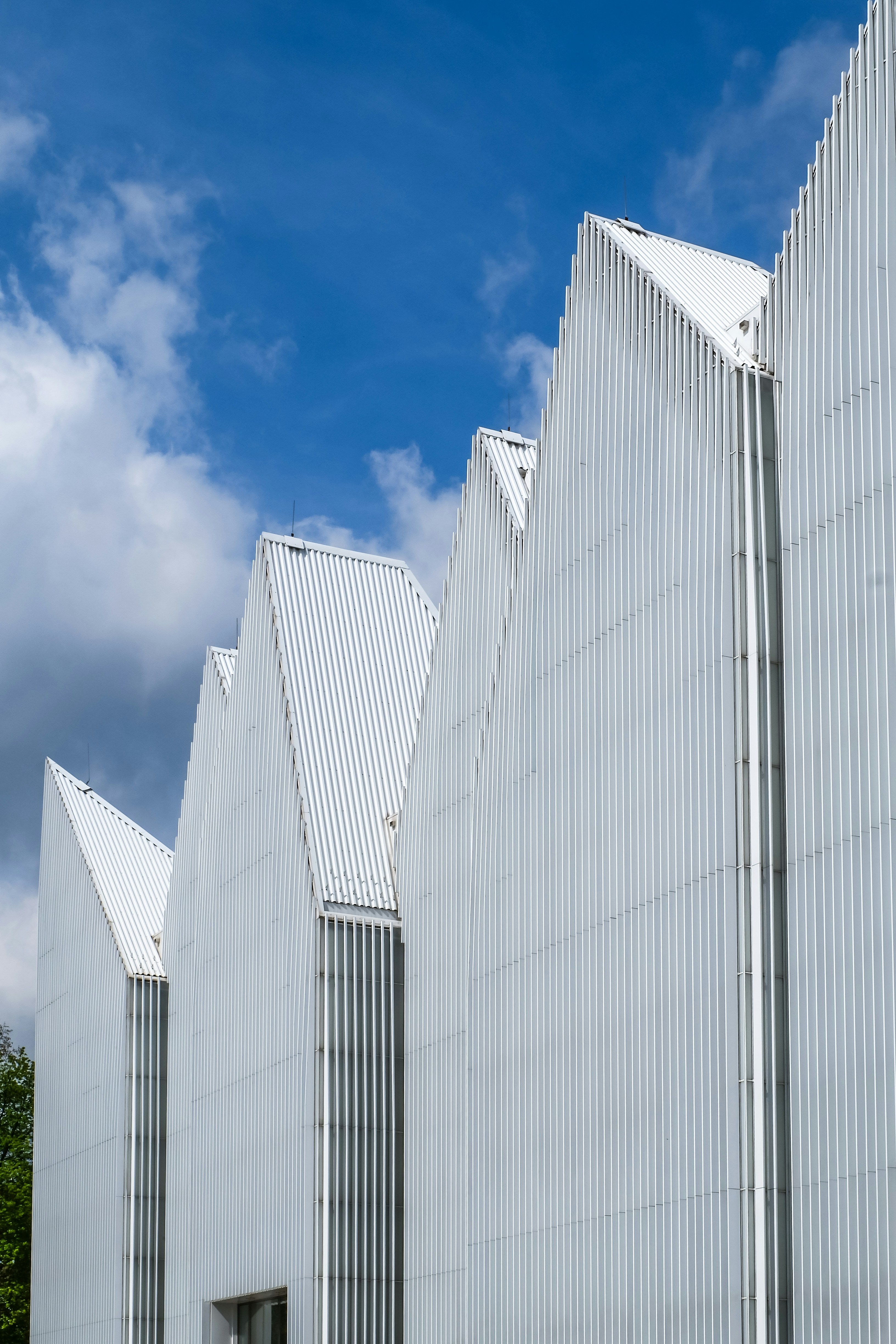 Angular white building facade with prominent peaks under a blue sky, showcasing contemporary architectural style.