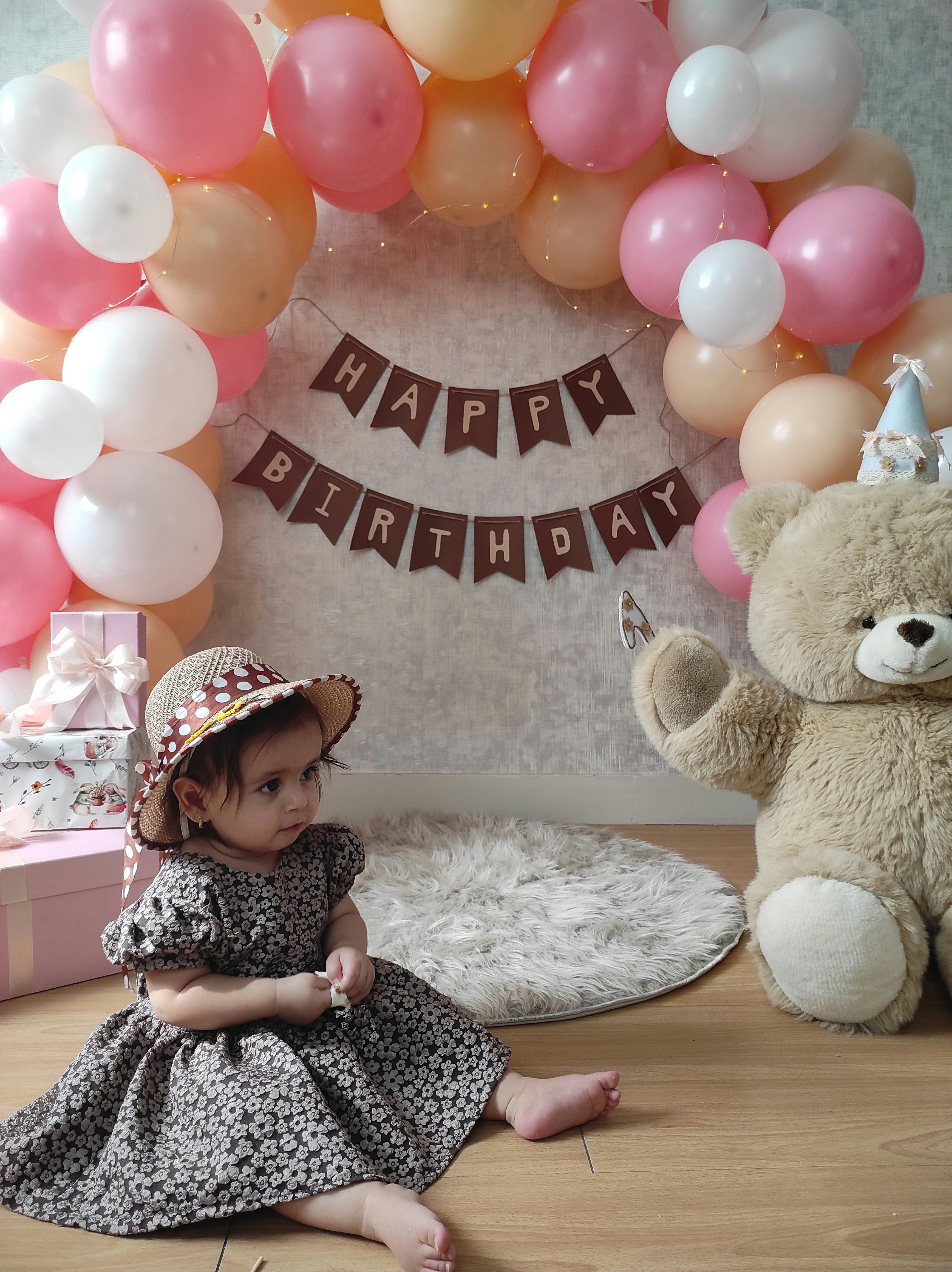A little girl sitting on the floor in front of a birthday arch