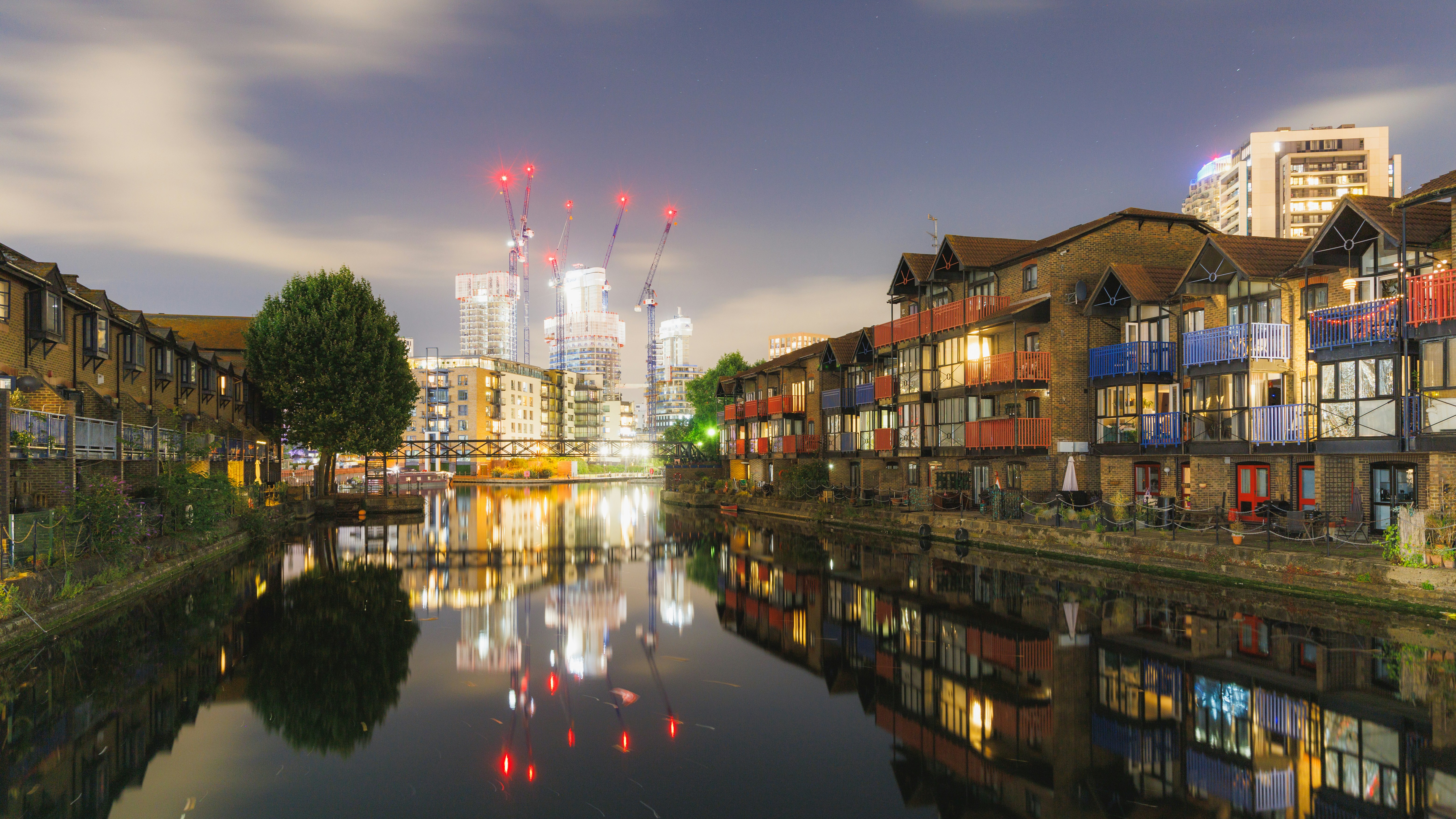 Night Canal Confluence: Brick Warehouses, Calm Reflections, and a Distant Crane Skyline