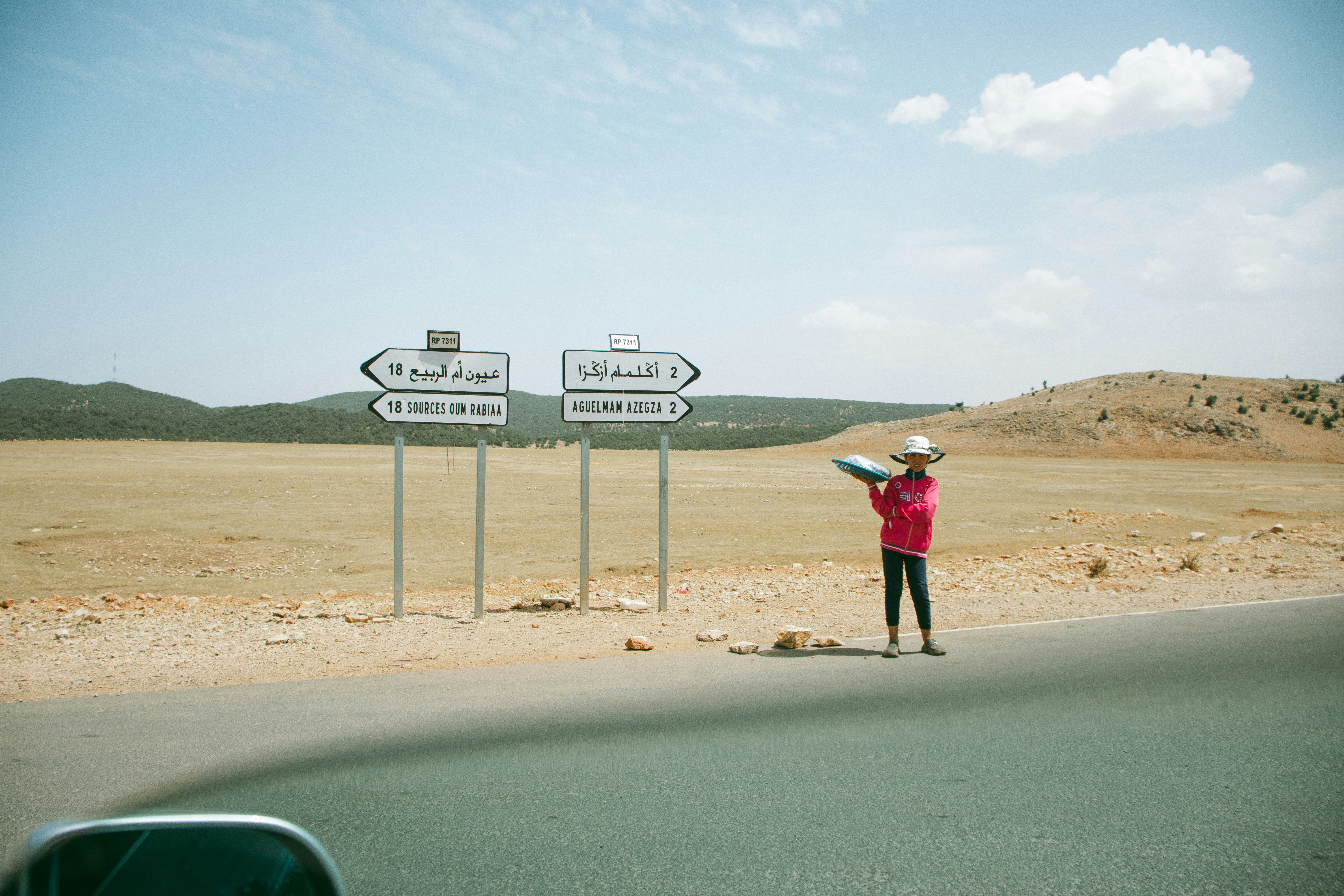 A man standing on the side of a road next to a road sign photo – Free ...