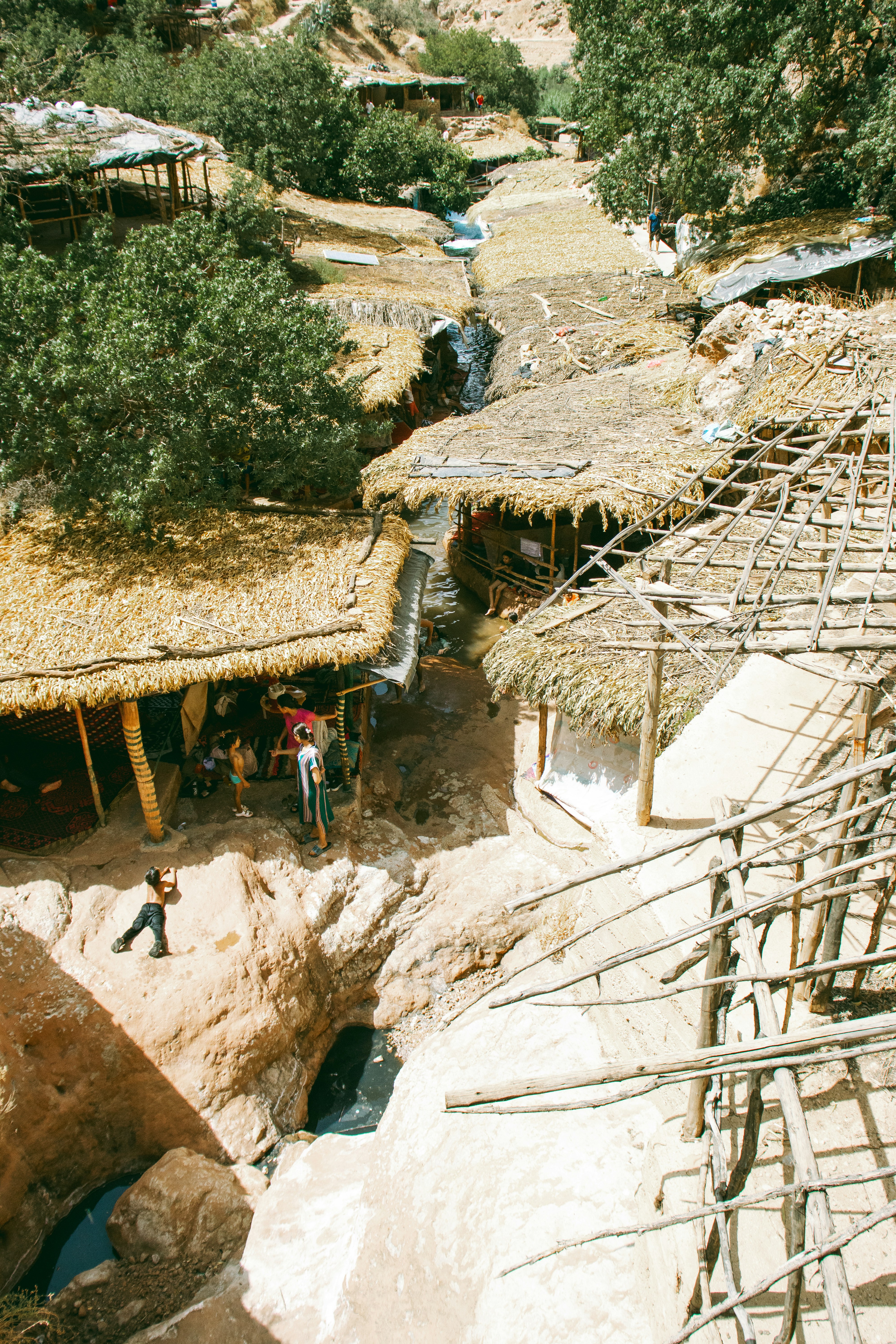 Sunlit hillside hamlet: thatch-roof huts and bamboo bridges over a rocky ravine