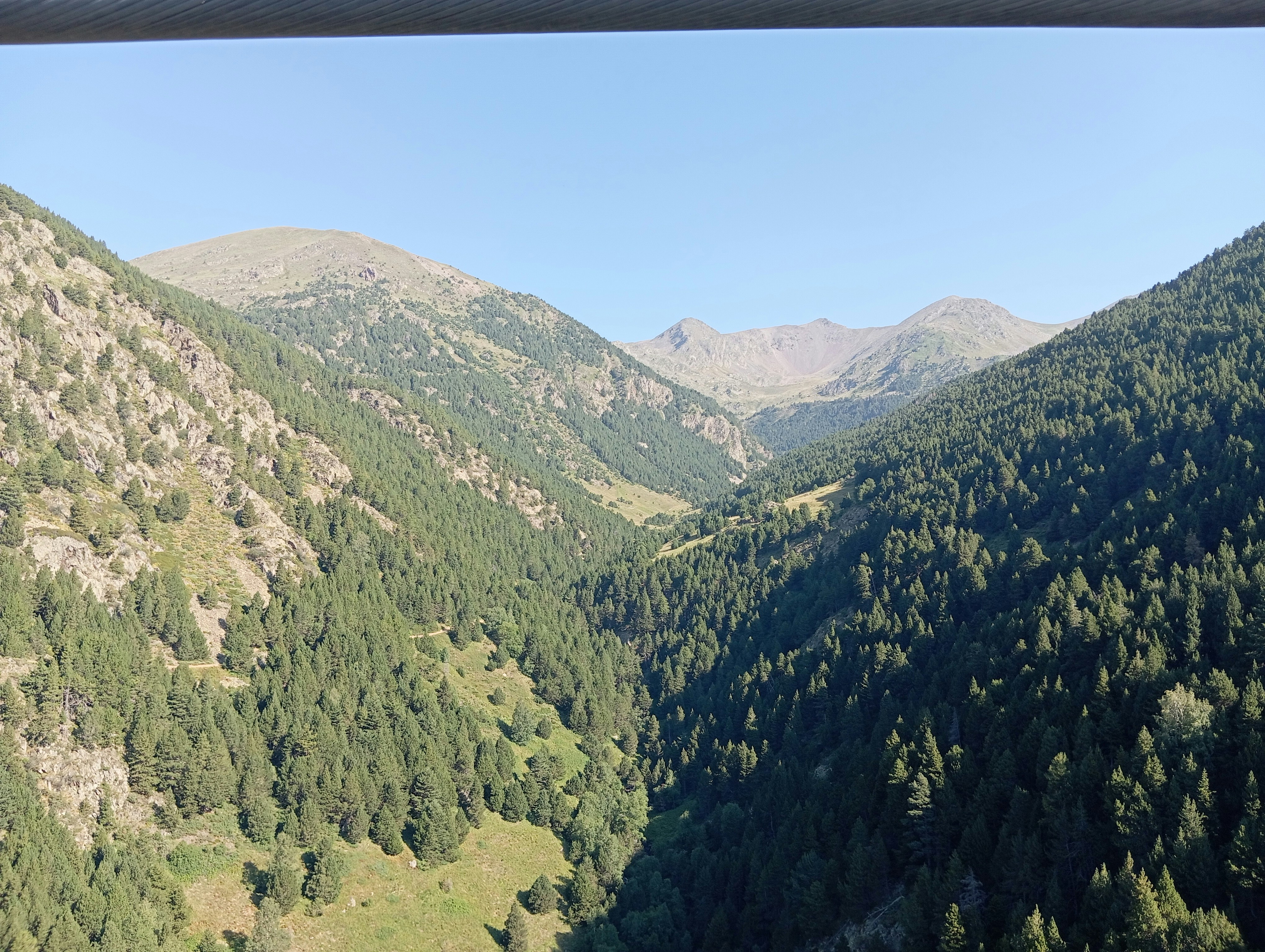 Lush green valley flanked by rugged mountains under a bright blue sky.