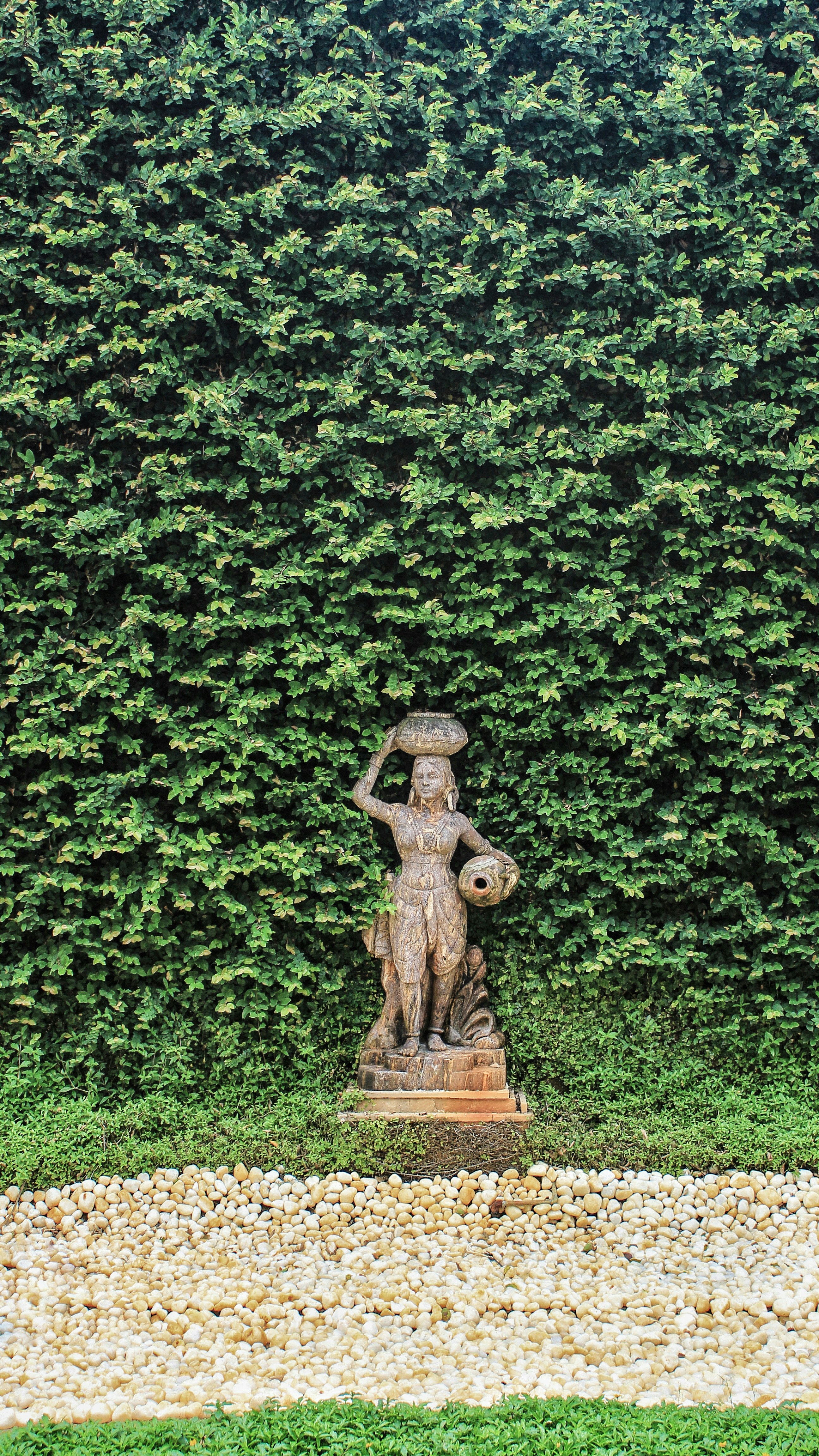 Balancing Duty: Stone Figure Before a Velvet Green Hedge