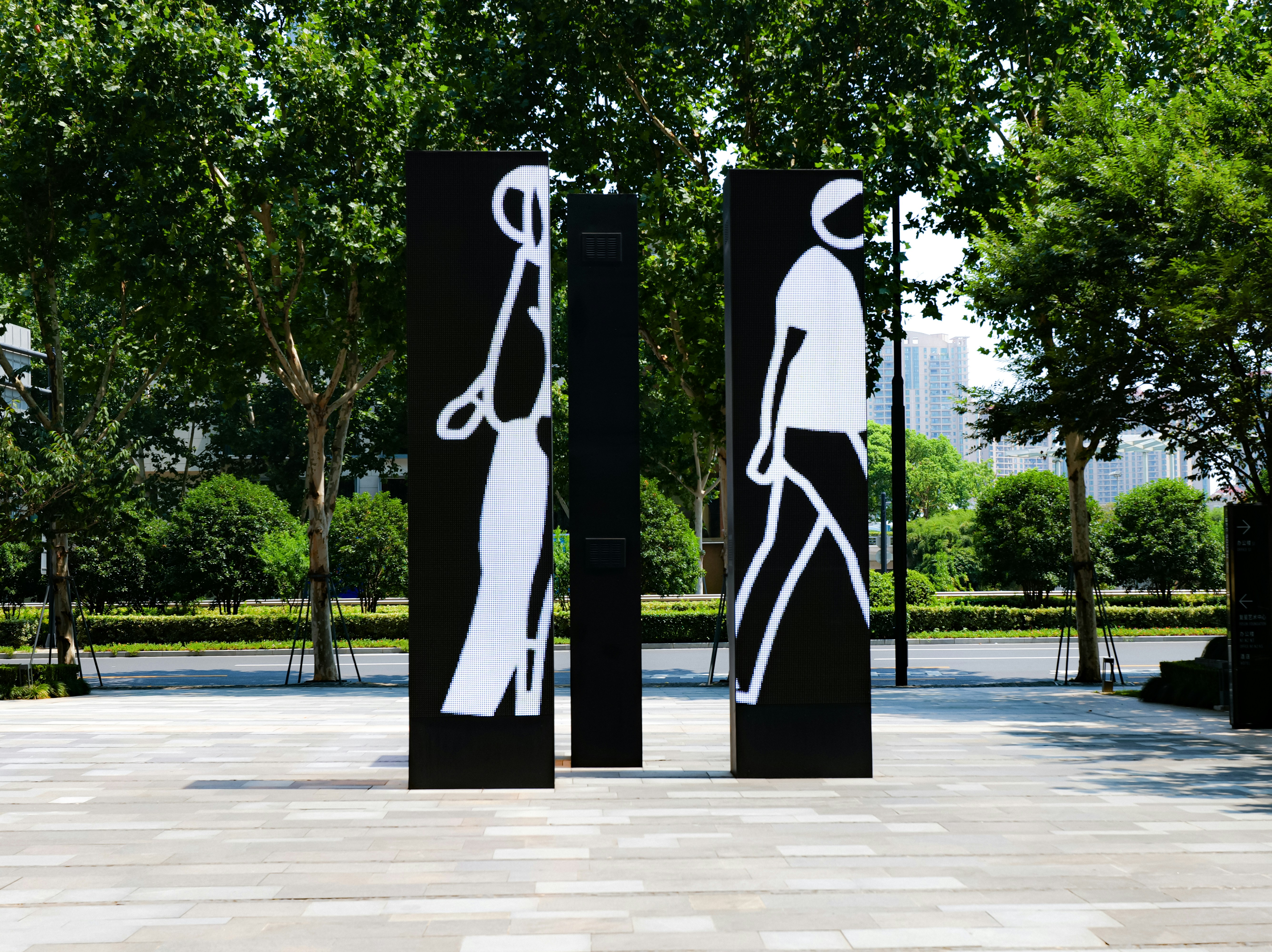 Monoliths of Motion: White silhouettes on black panels in a sunlit plaza