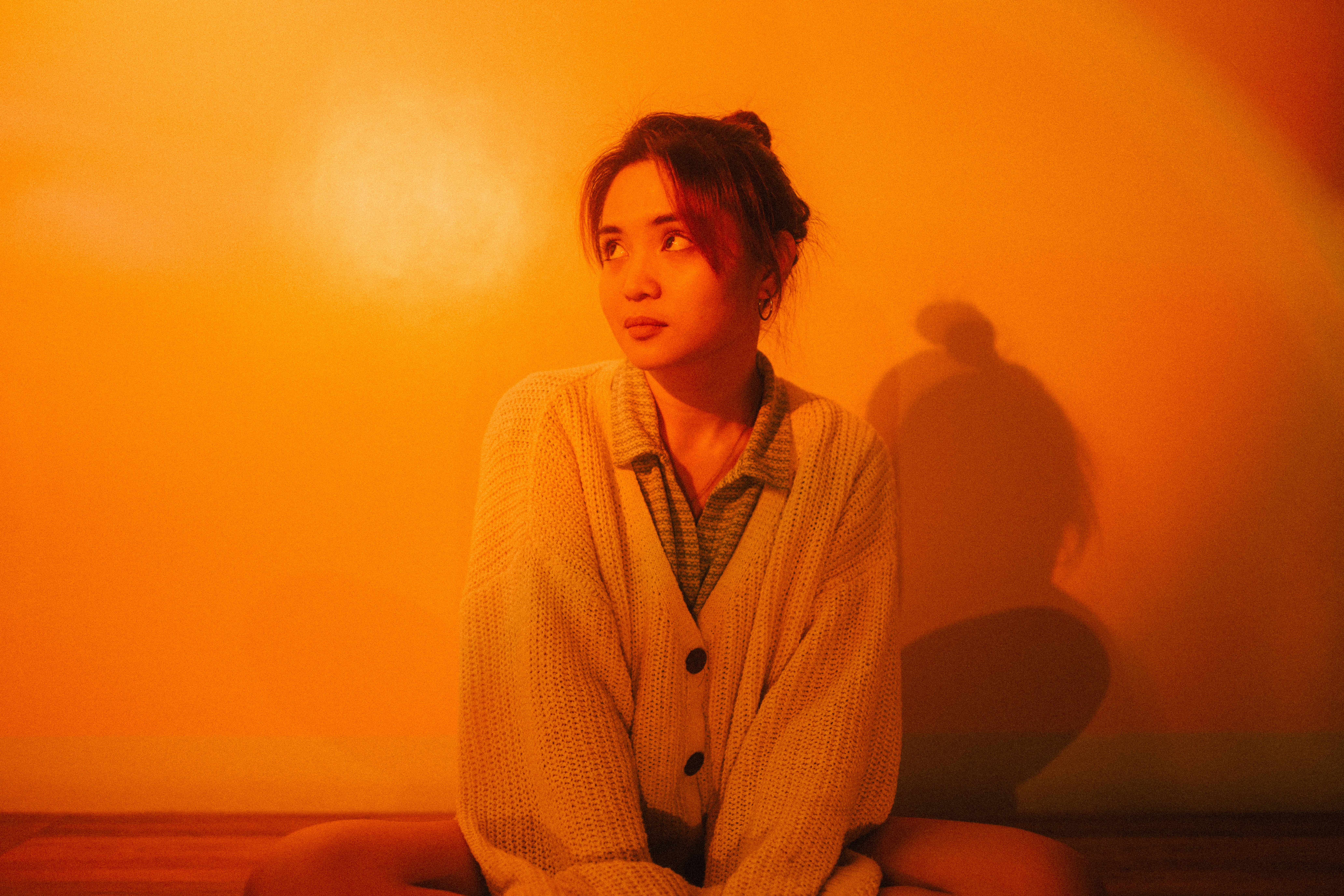 Person sitting against a wall bathed in soft amber lighting, casting a shadow that adds depth to the scene.