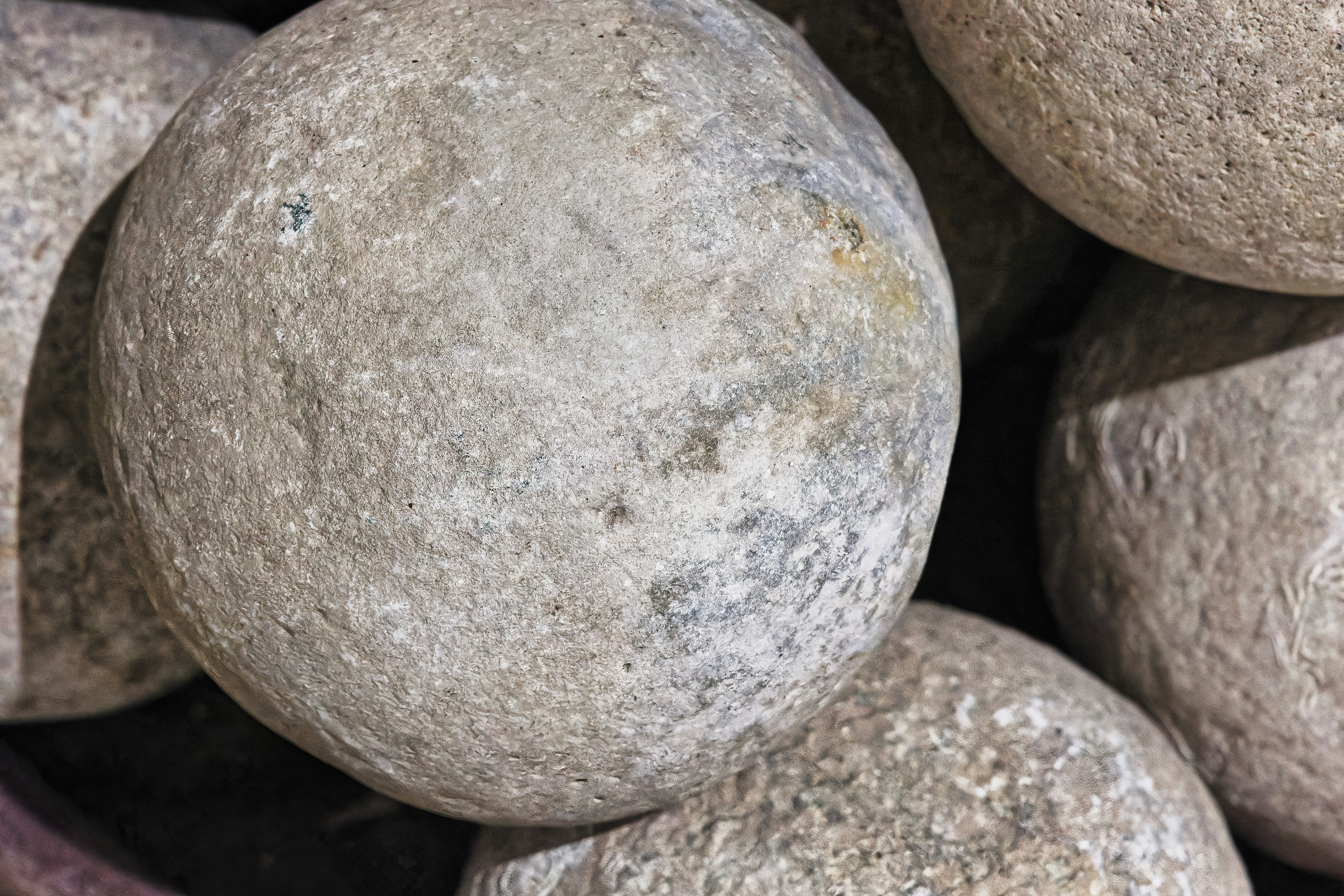Weathered stones arranged in a pile at a rustic outdoor location during daylight - A collection of smooth, rounded stones of varying sizes sits in a rustic setting under natural light.