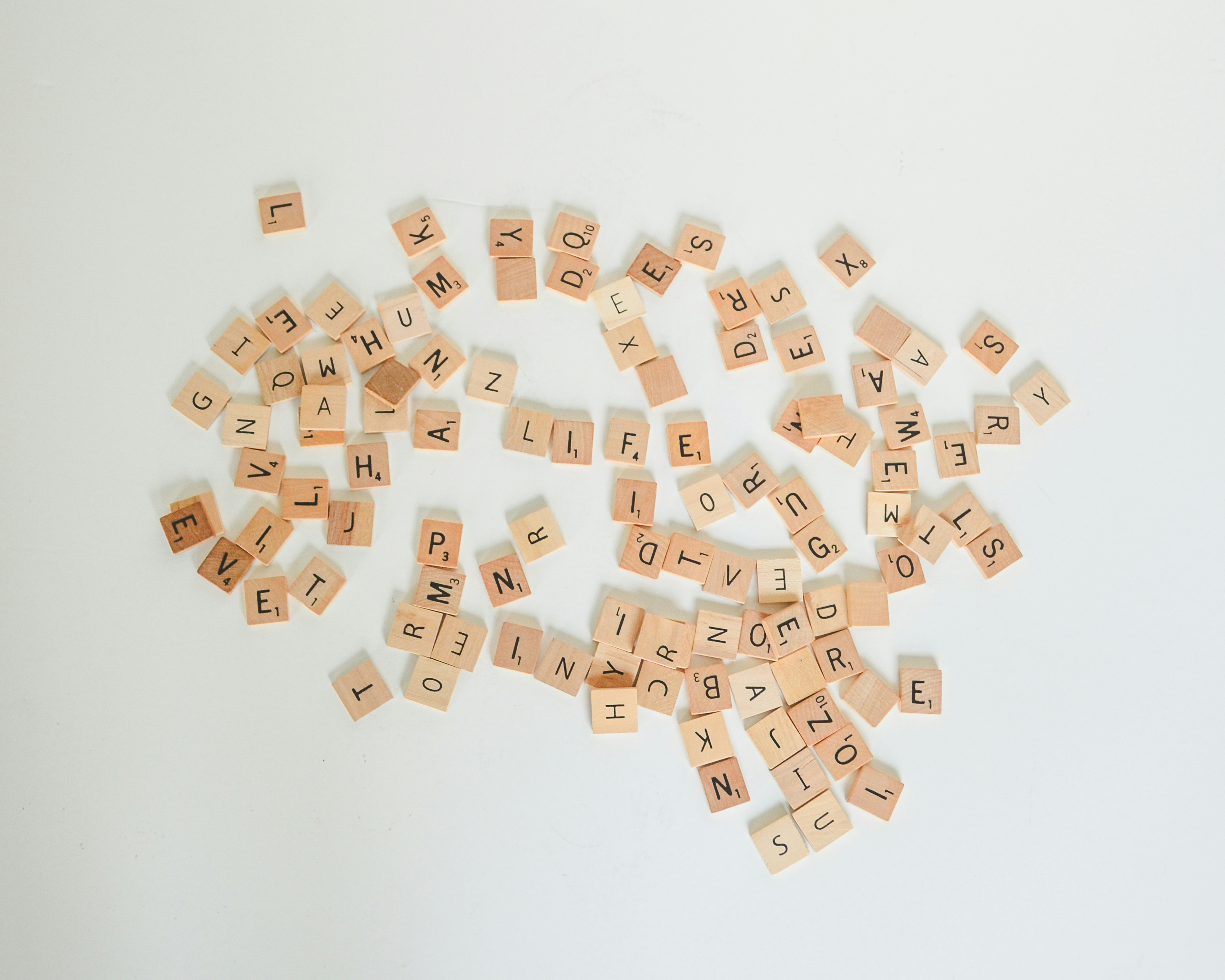 Scrabble Fragments: pale-wood letters drift across a white plane