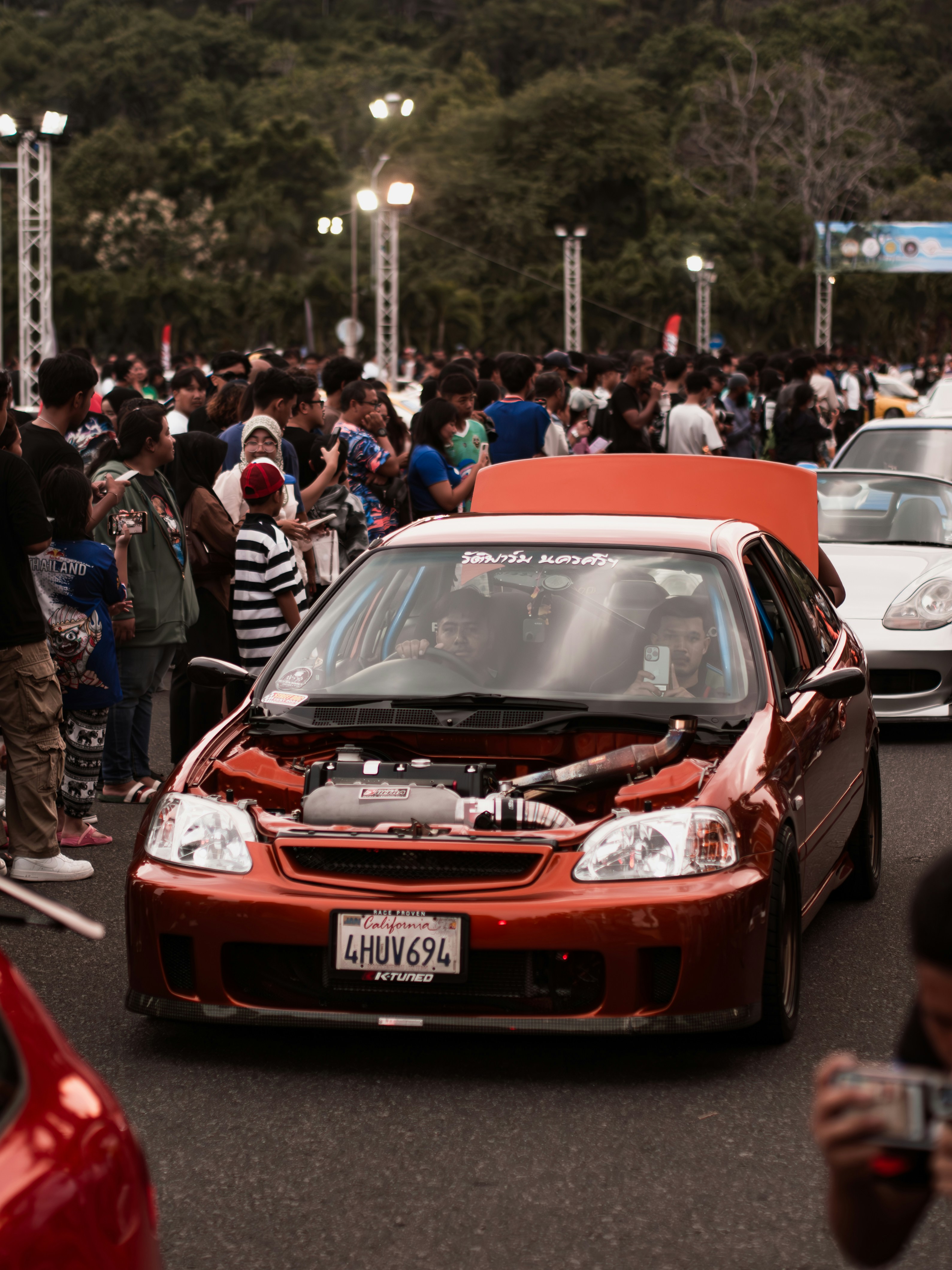 A group of cars driving down a street next to a crowd of people photo ...
