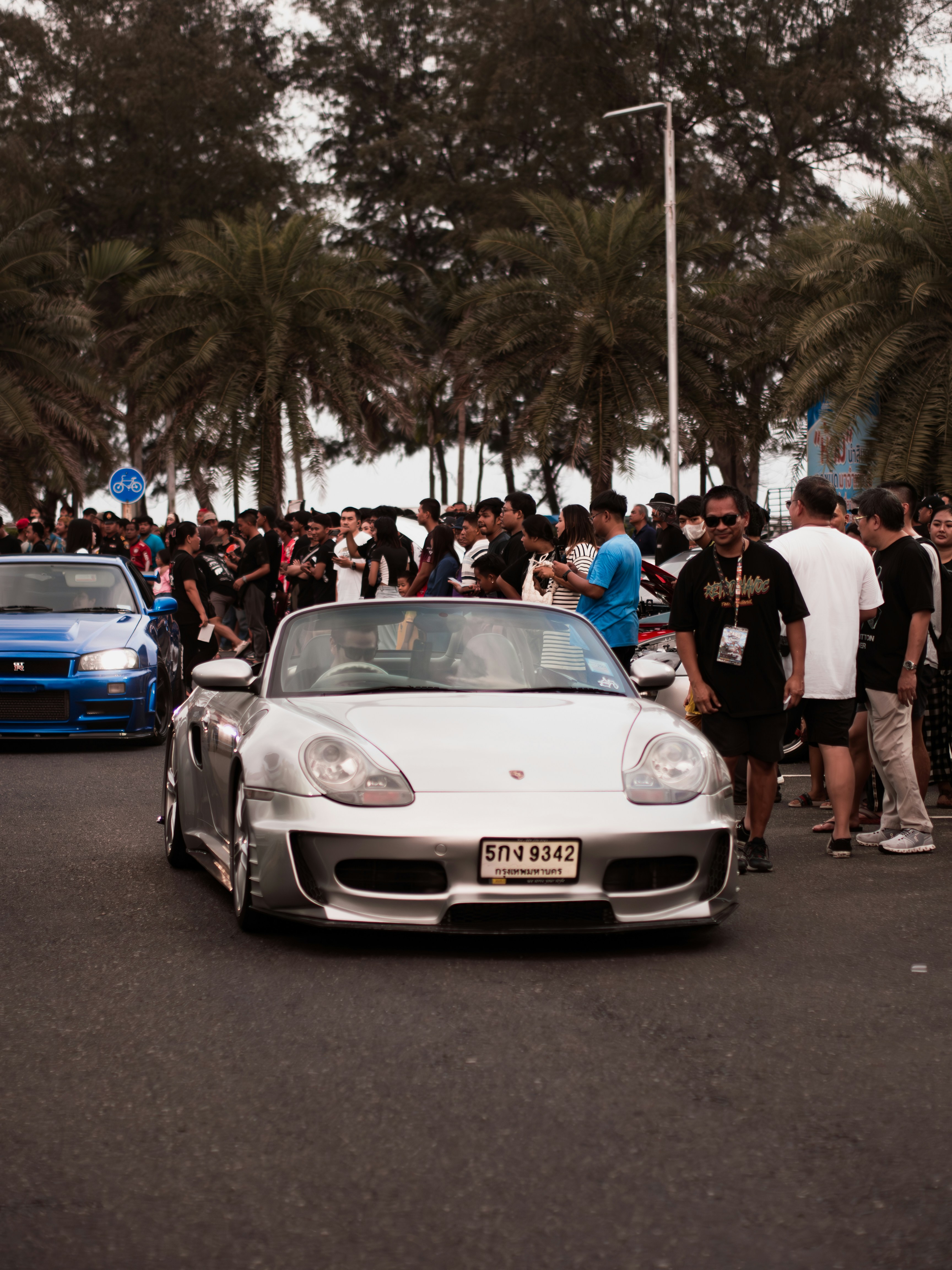A white sports car driving down a street next to a crowd of people ...
