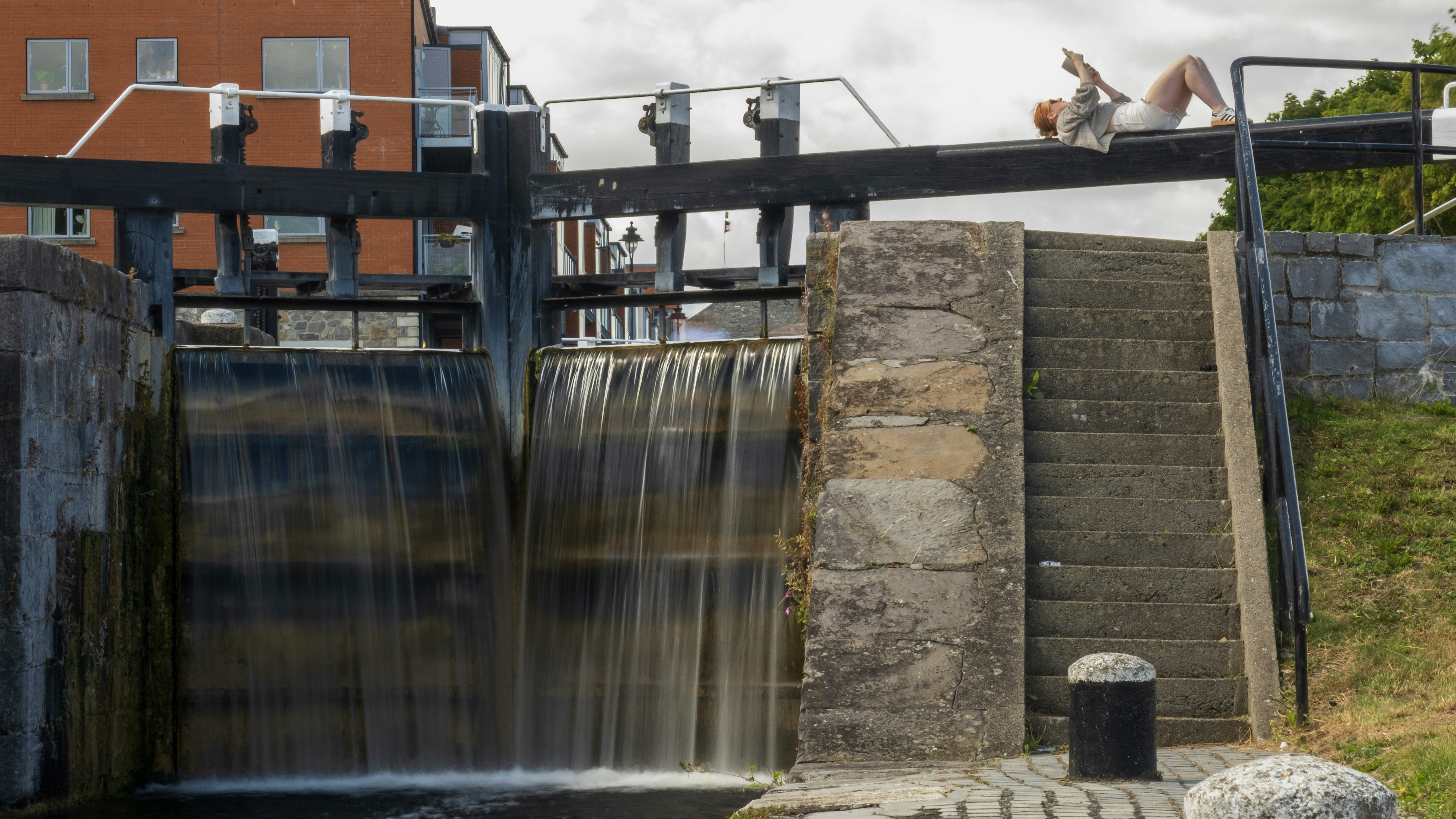 A women laying down in a brick wall reading a book by a lock on the Grand Canal in Dublin, Ireland