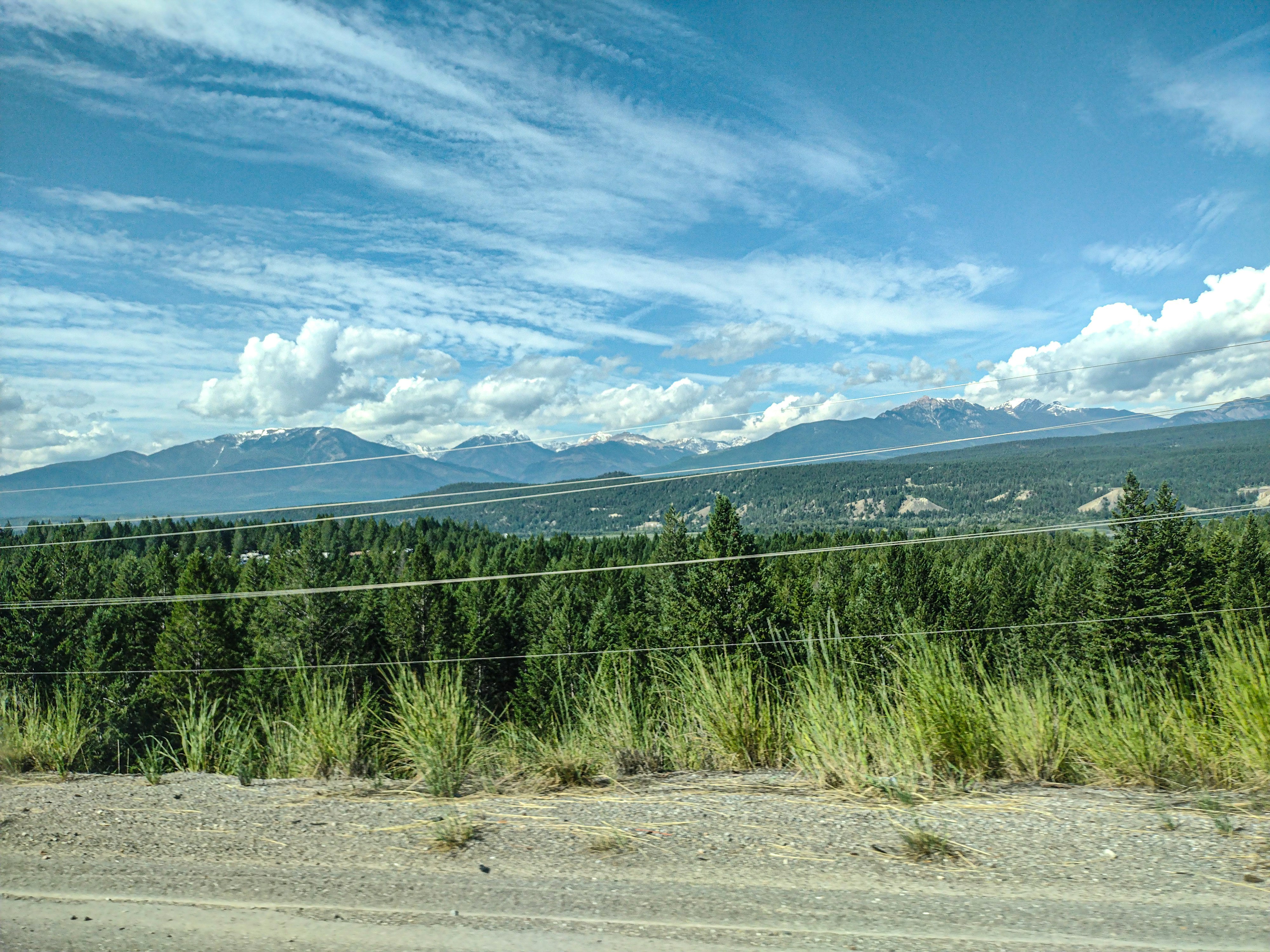 Distant snow-capped mountains frame a sagebrush foreground, with power lines sweeping the scene under a bright blue sky.