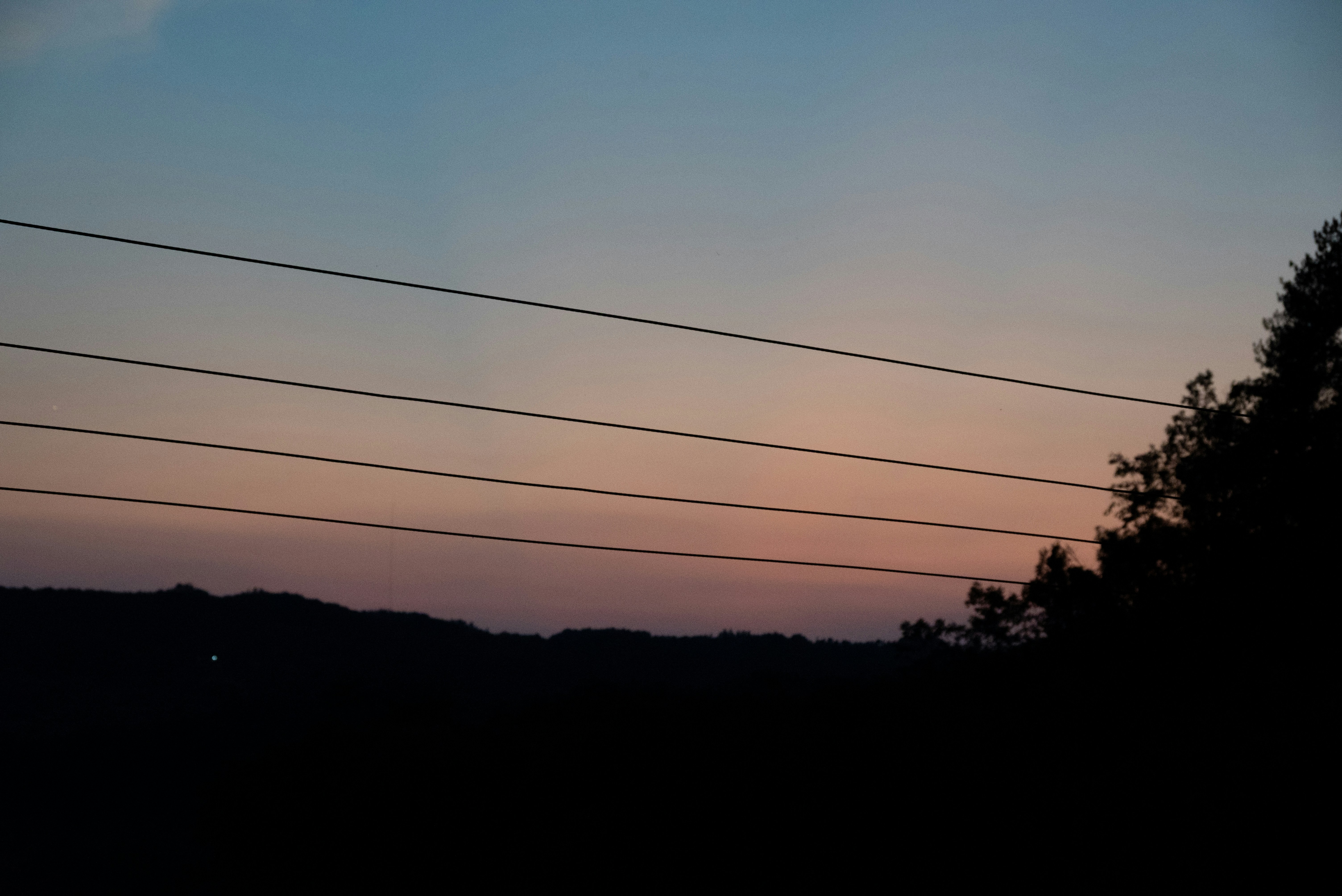 Subtle gradient of twilight colors fading into the horizon, framed by silhouetted power lines and distant hills.