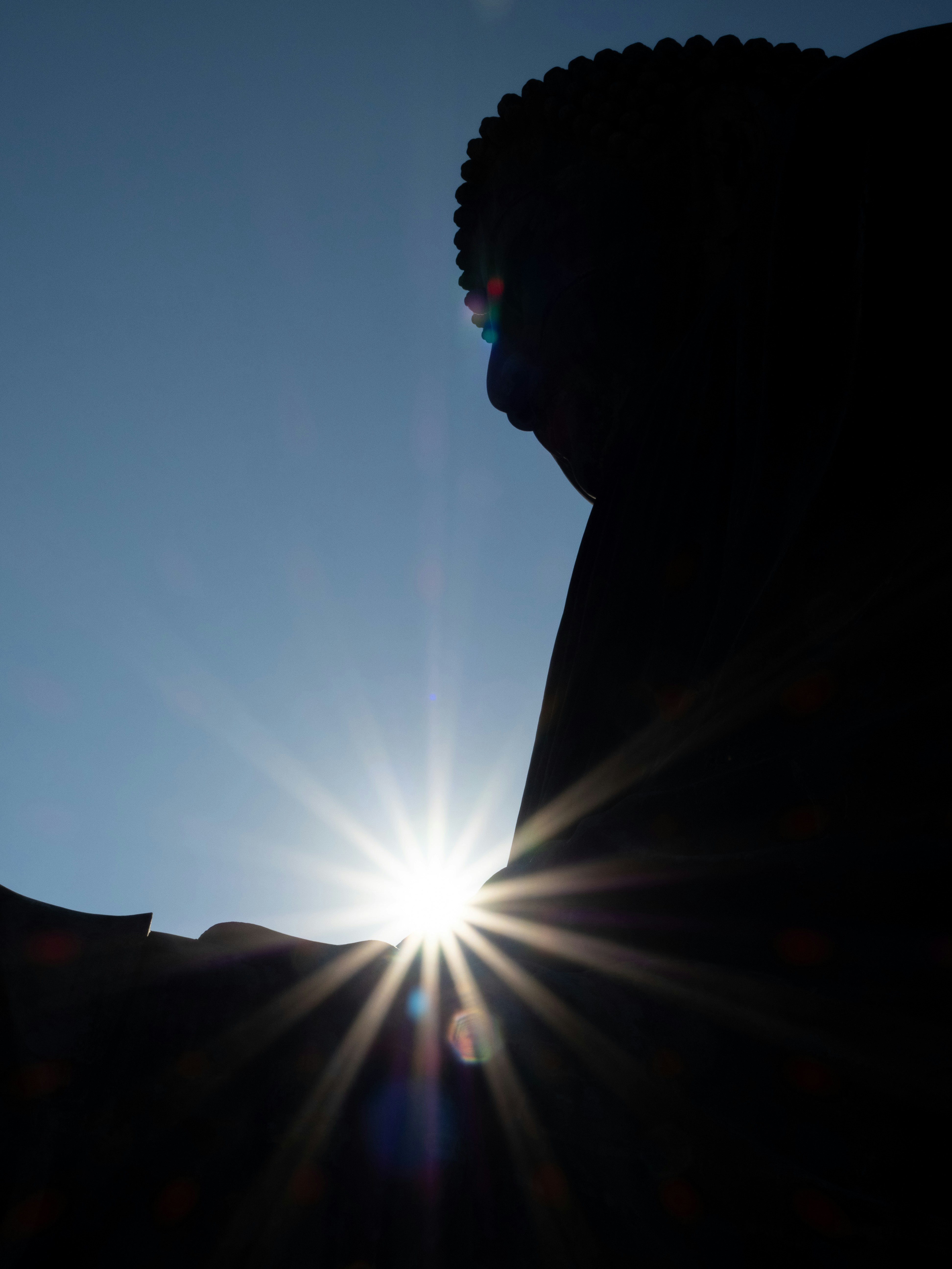 The sun shines brightly through the silhouette of a statue