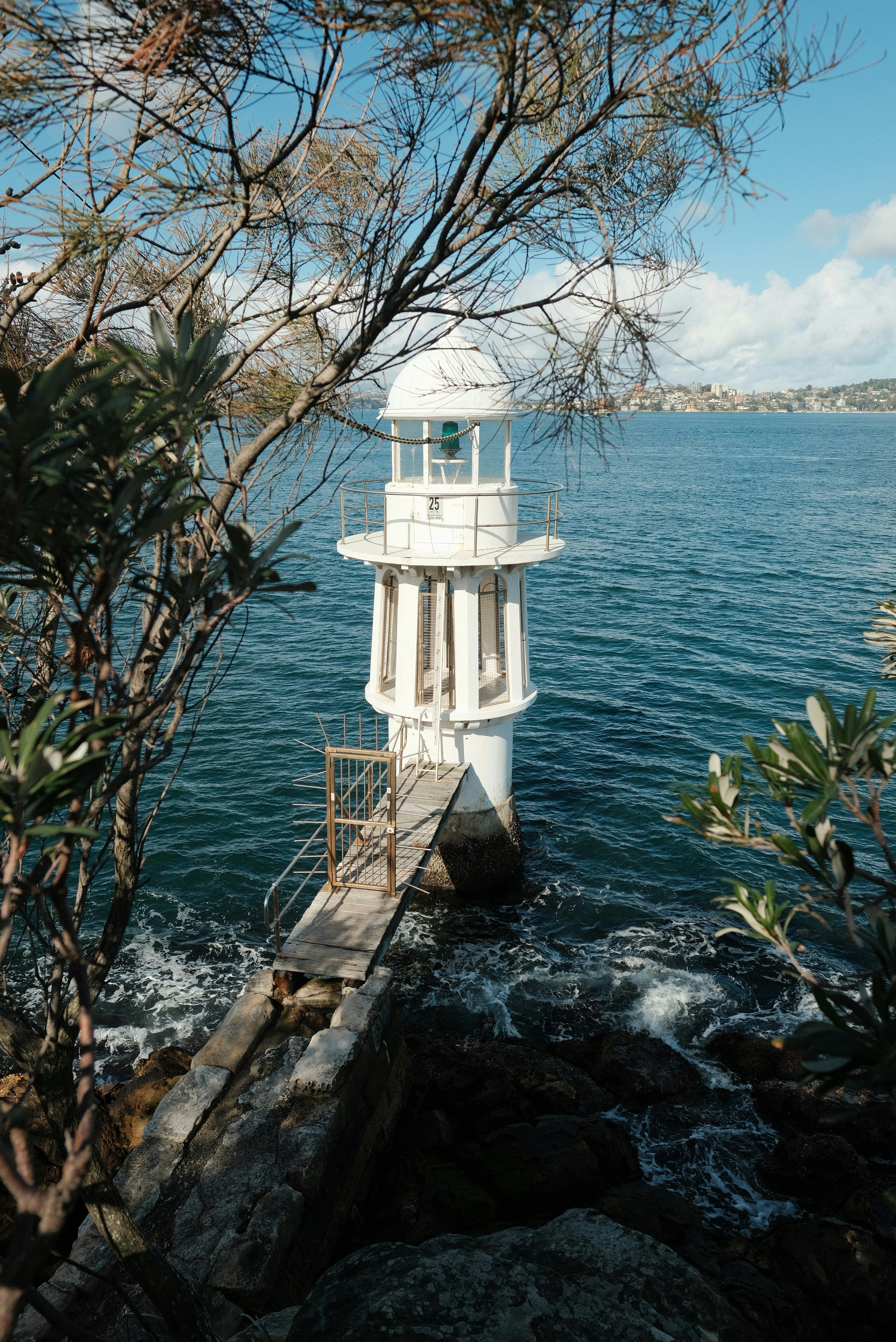 A white lighthouse stands on a rocky shore, surrounded by greenery and gently lapping waves, symbolizing maritime safety.