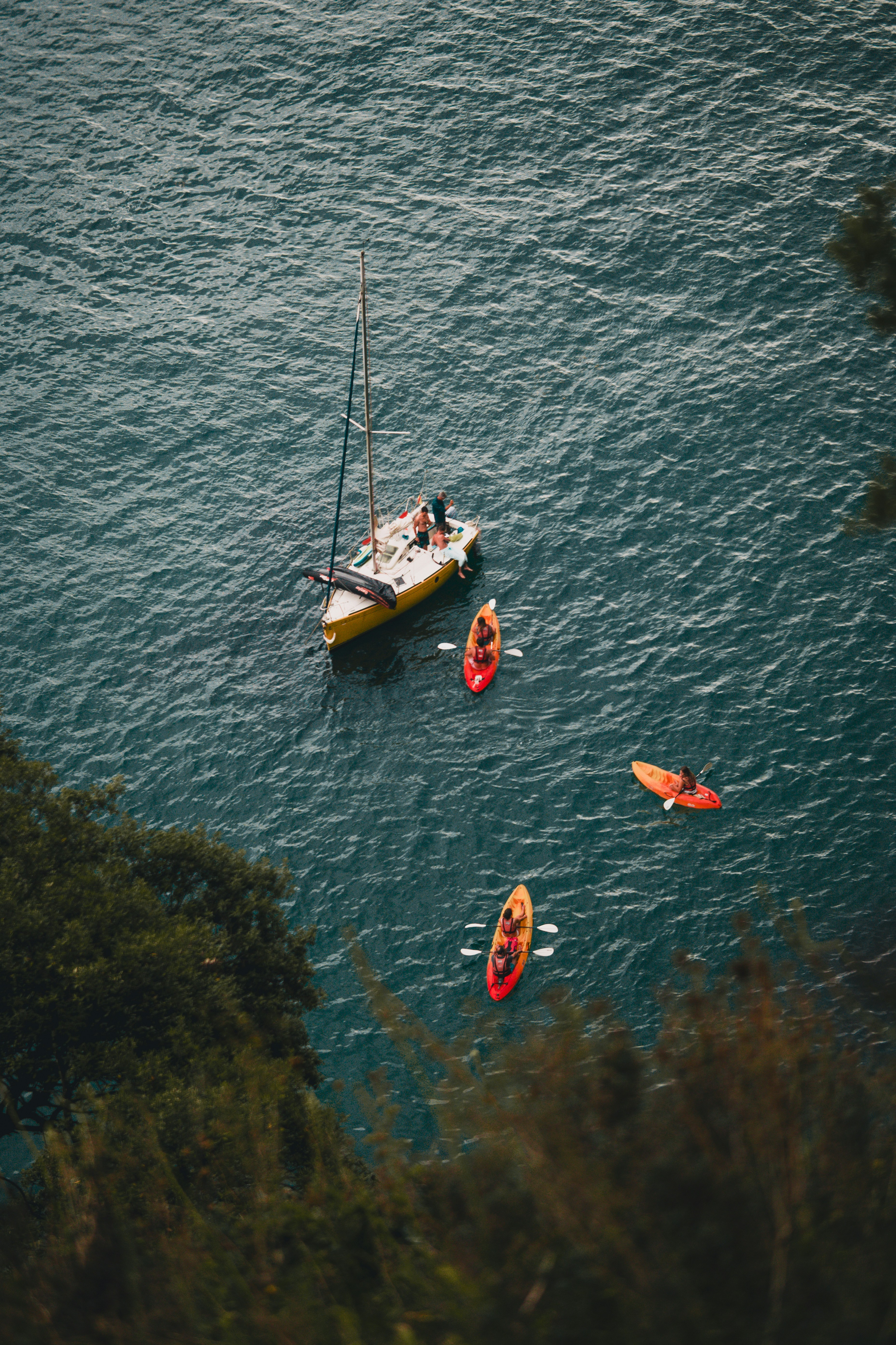 A sailboat and colorful kayaks navigate tranquil waters, surrounded by lush greenery. The scene captures the essence of outdoor leisure.