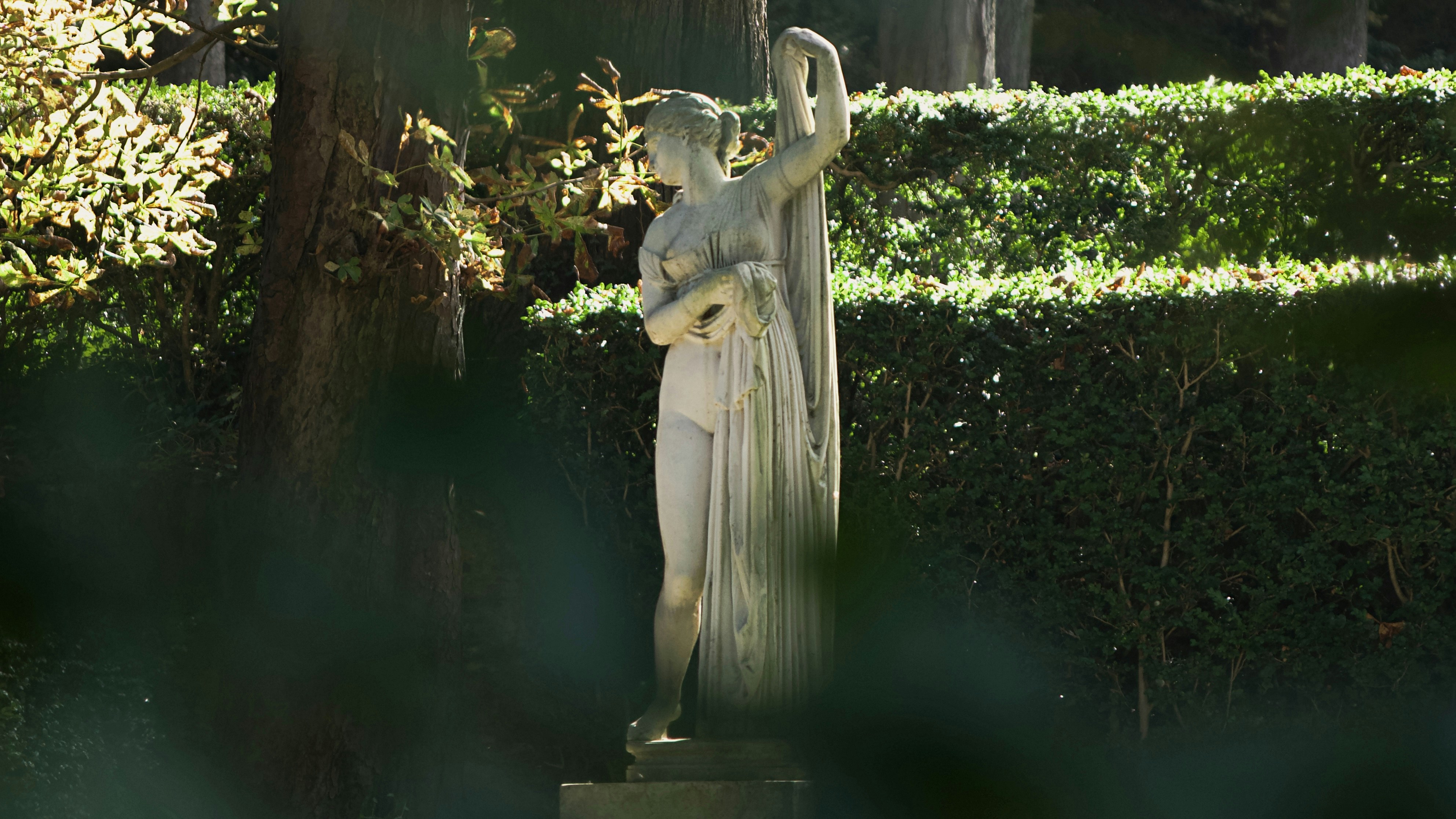 Stone statue of a woman holding a bird, surrounded by lush greenery.