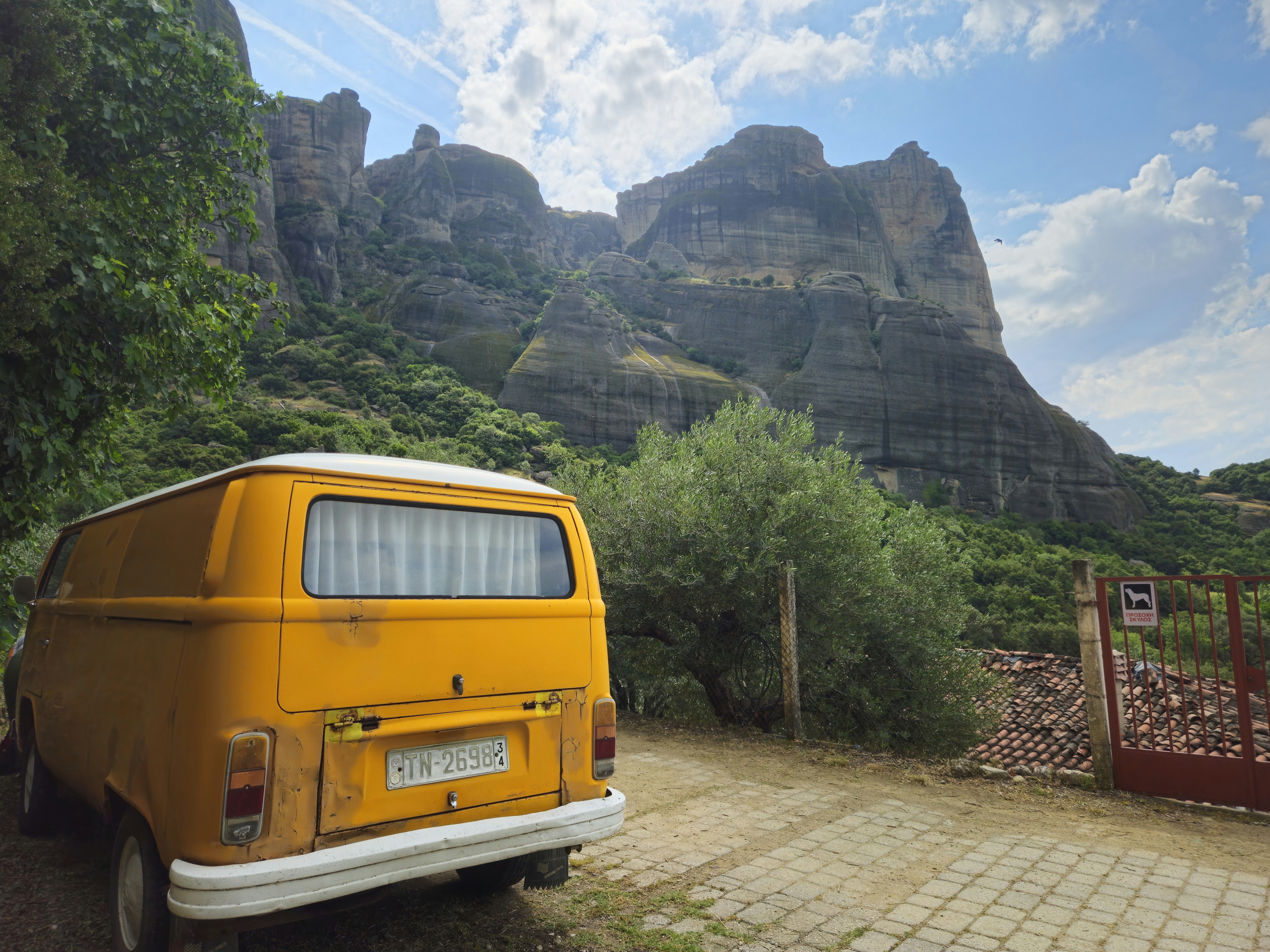 Yellow van parked near lush greenery with towering rock formations in the background.