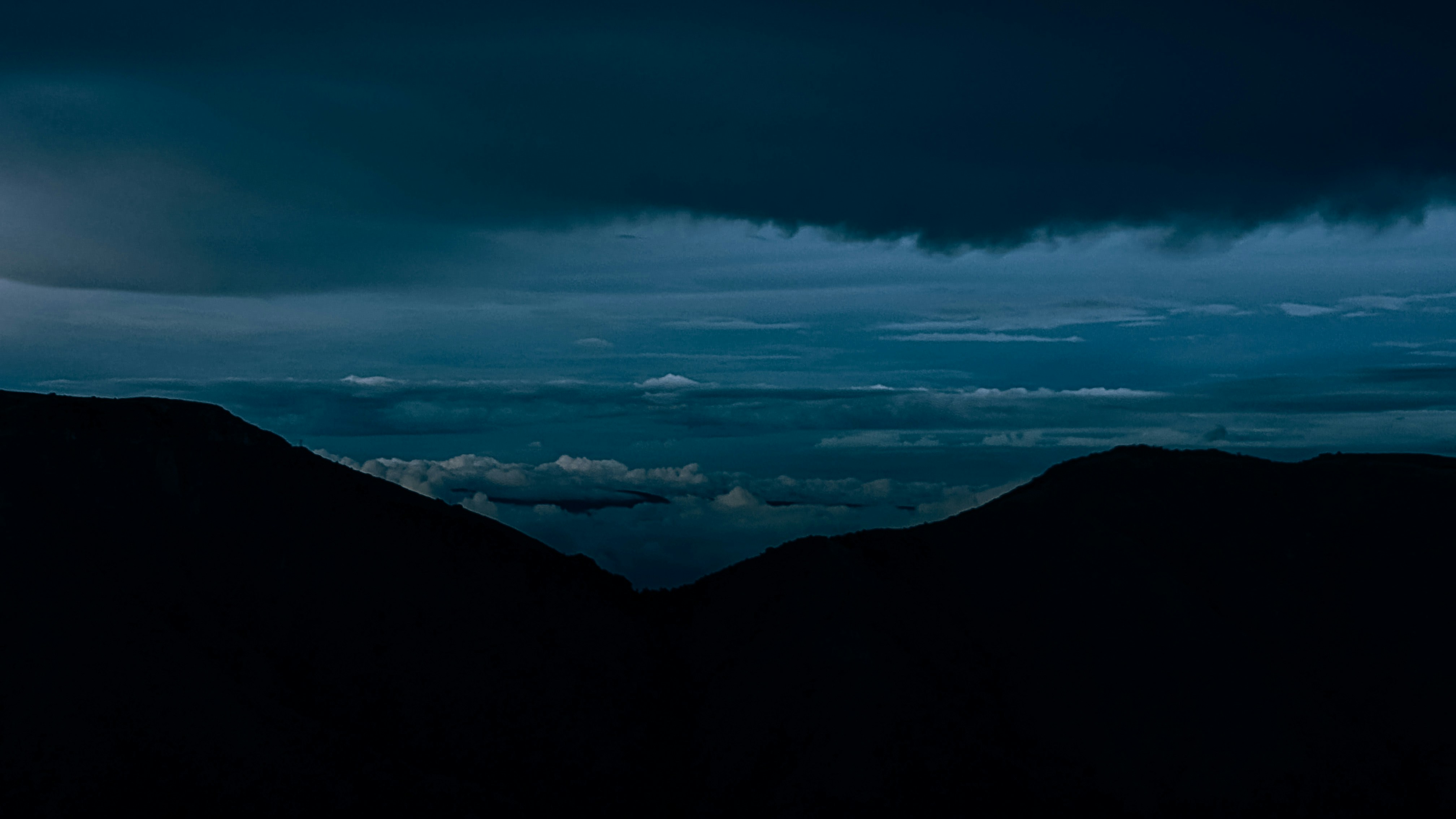 Silhouetted mountain peaks under a moody twilight sky with layered clouds and hints of fading light.