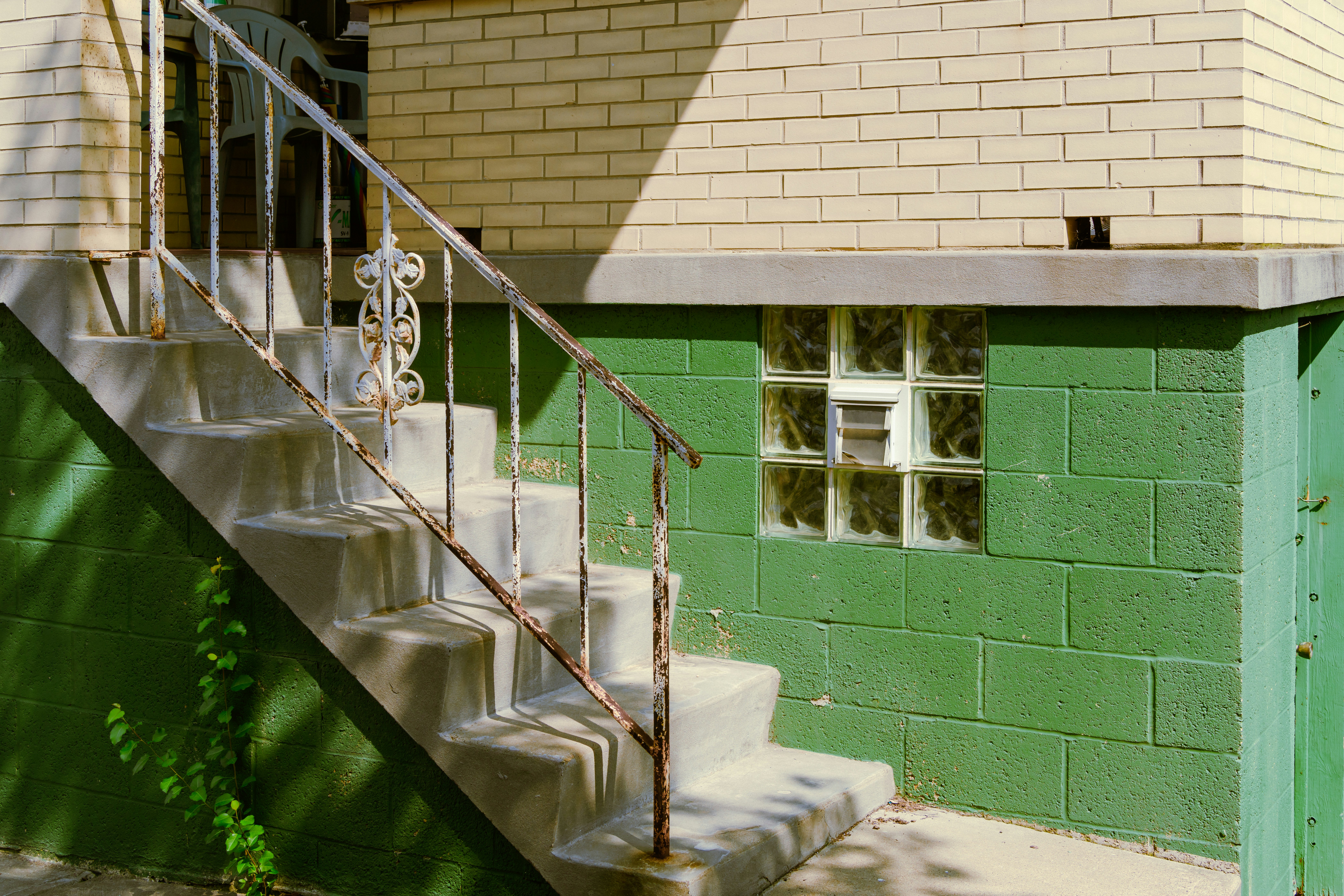 Concrete stairs with a metal railing lead to a brick building, accentuated by green-painted masonry and glass block windows.