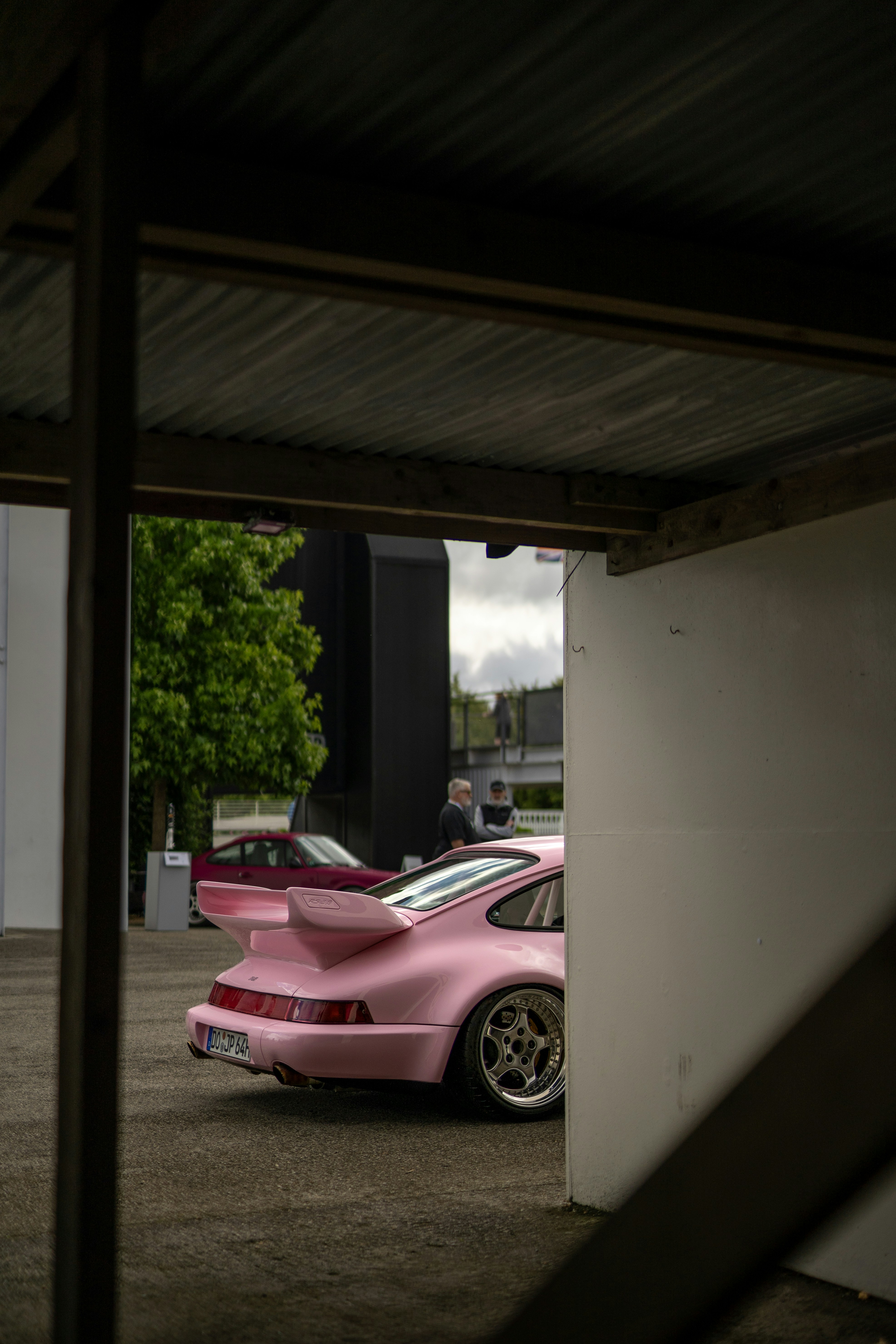 Pastel Pink Performance: A Winged Coupe Framed by Industrial Shadows