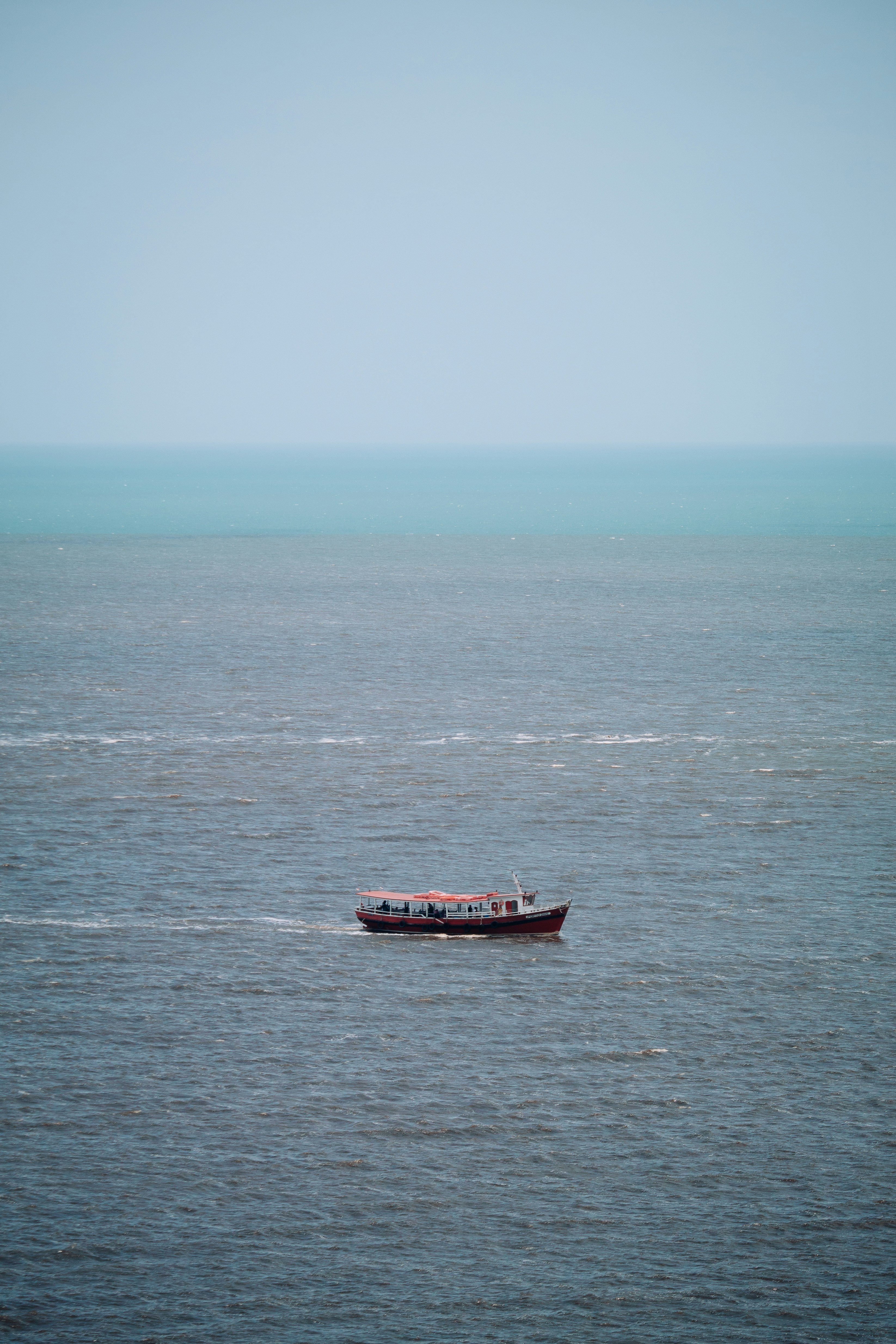 Red boat on a turquoise sea beneath a quiet horizon