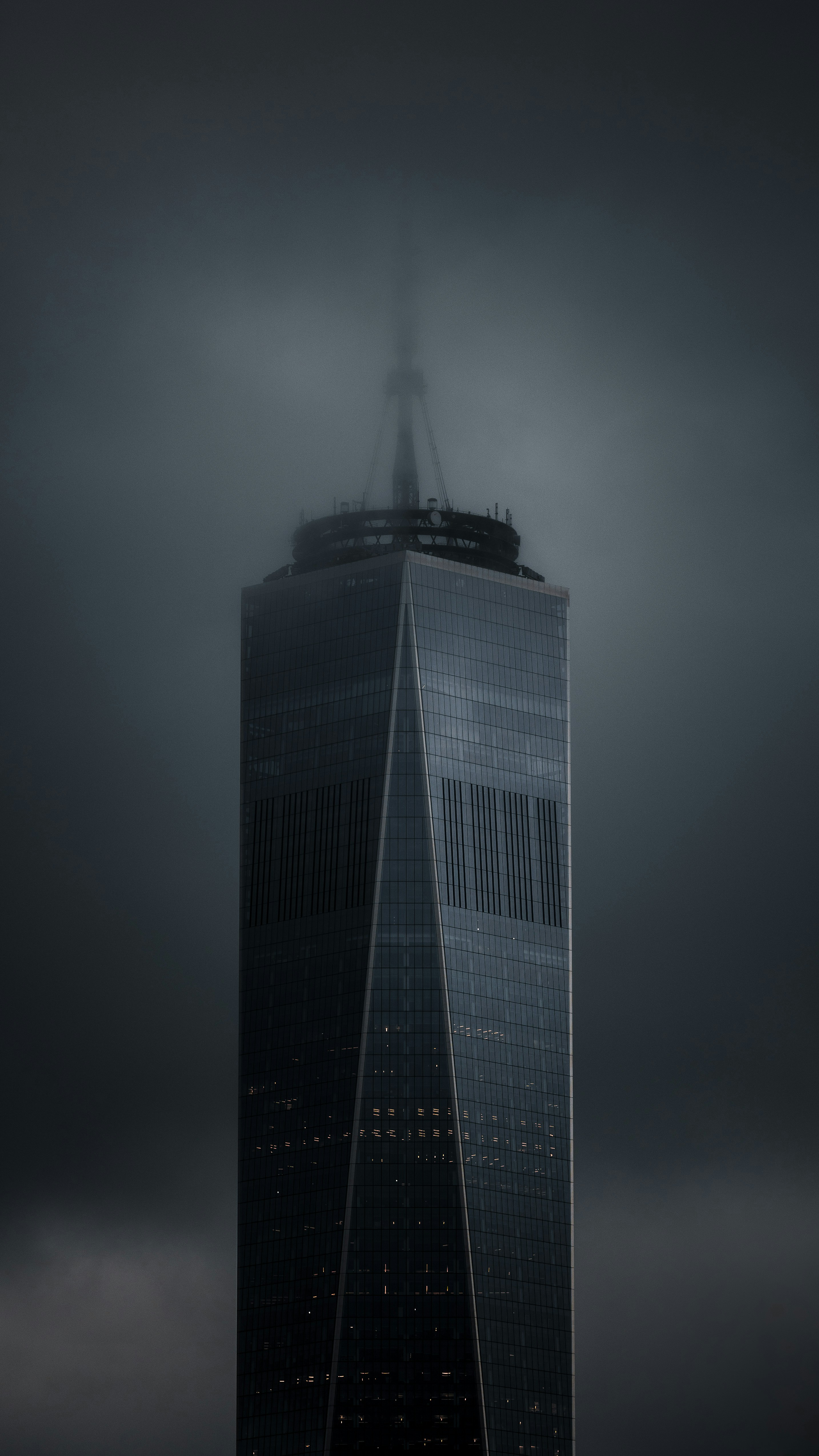 The One World Trade Center looms through a veil of mist and clouds, its sleek lines contrasting with the darkened sky. A testament to resilience and architectural prowess.