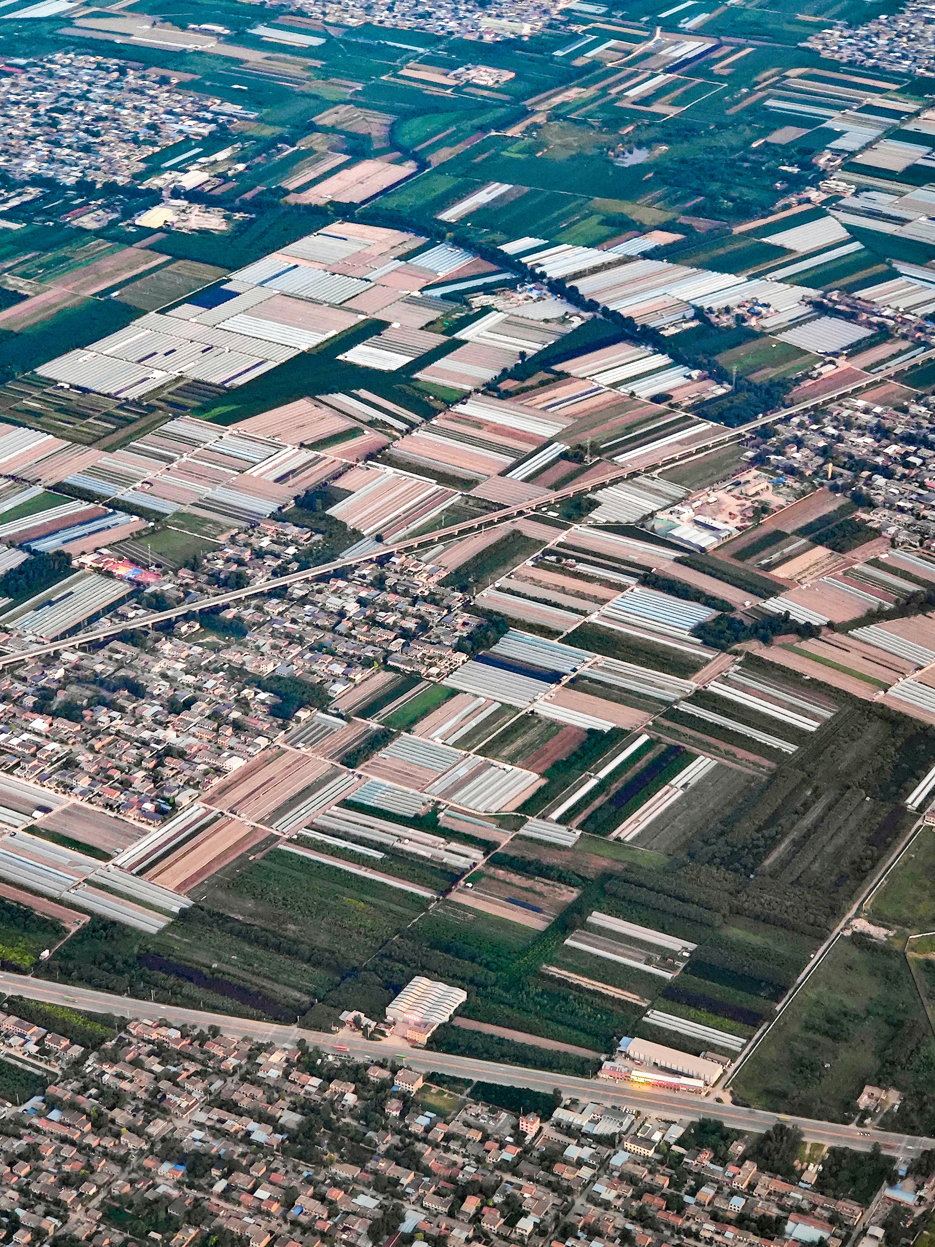 Expansive aerial view of agricultural fields interspersed with urban development, showcasing the intricate patterns of cultivation and land use.