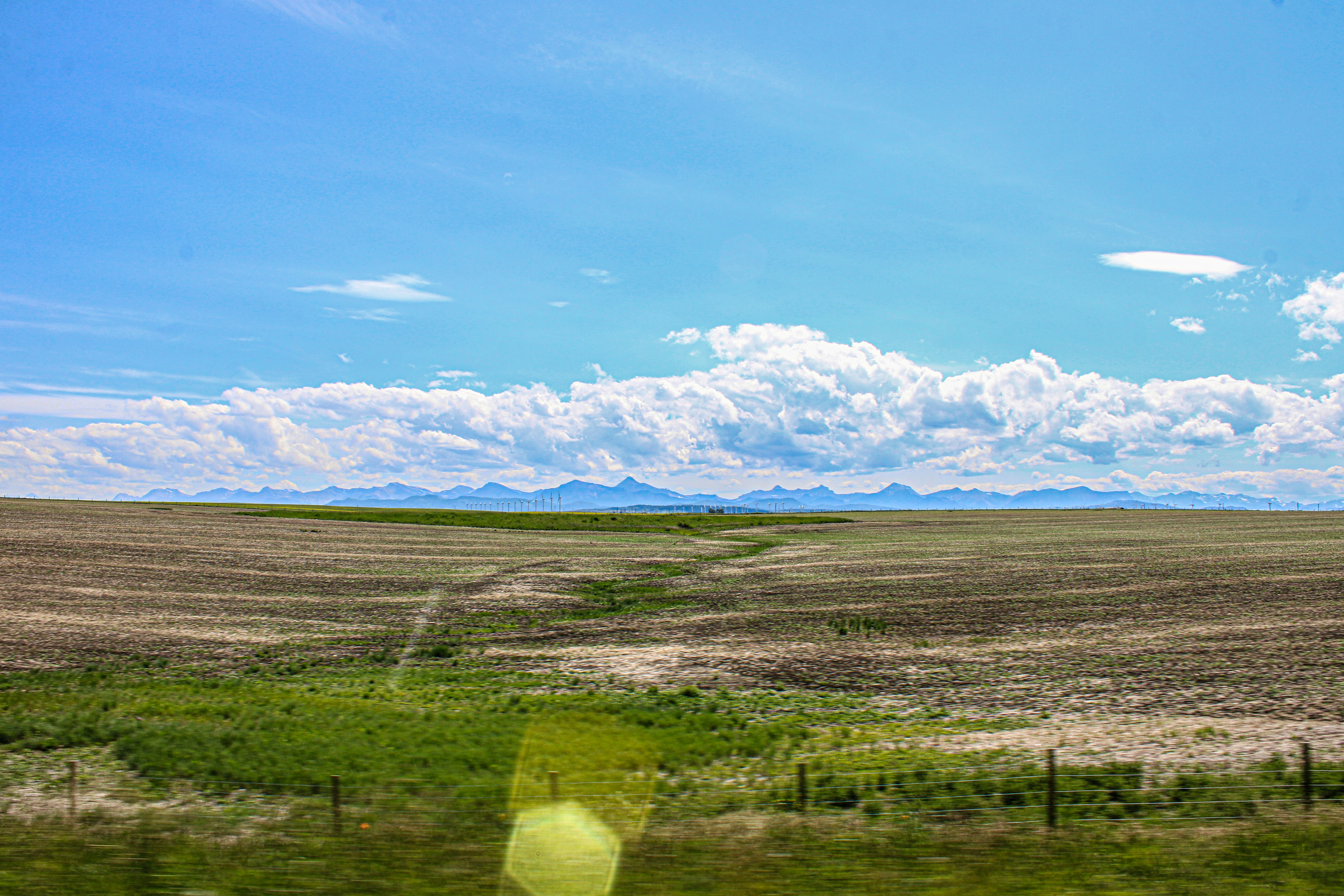 Vast agricultural fields stretch under a vibrant sky, with distant mountains creating a dramatic backdrop. The image captures the serene beauty of rural landscapes.