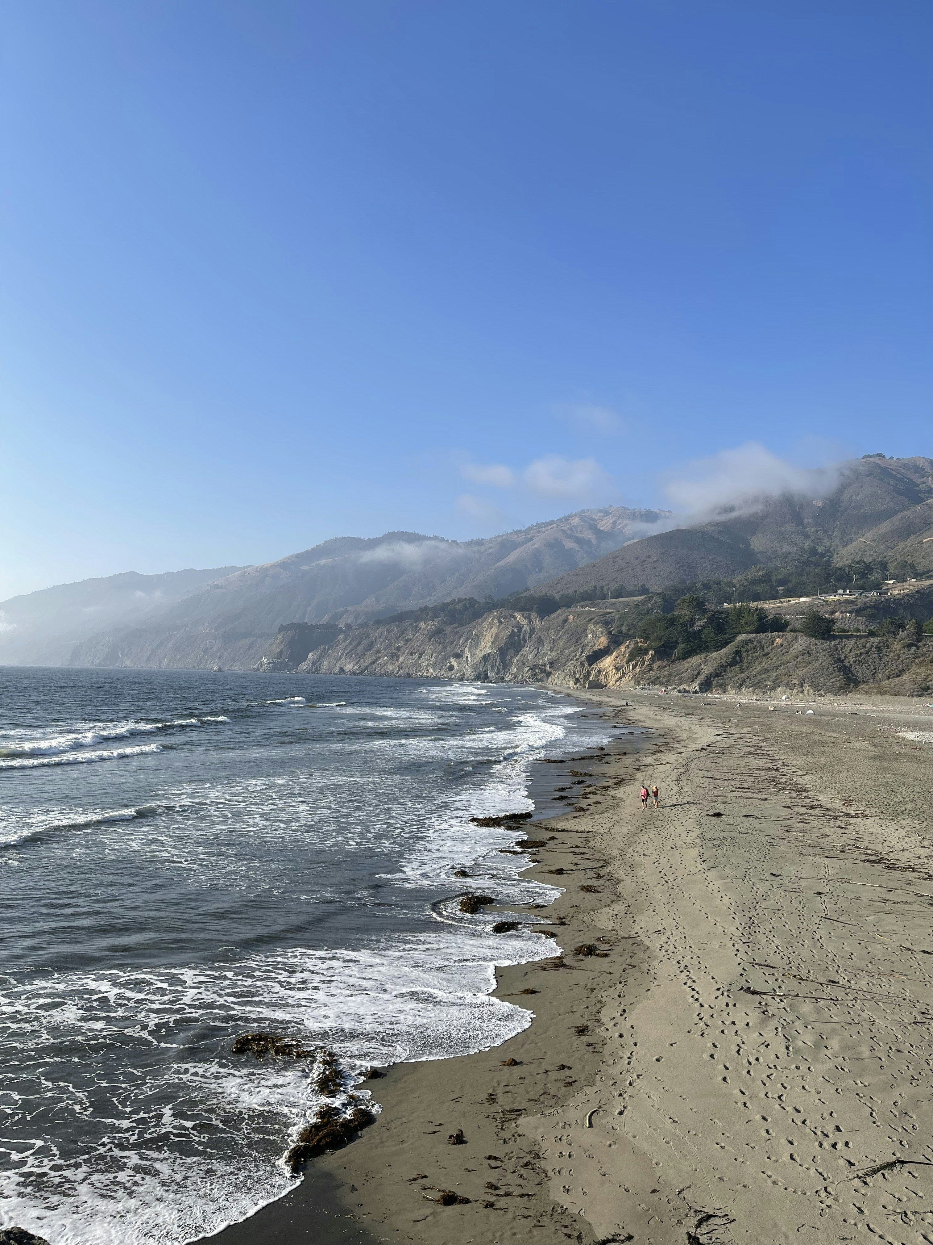 Gentle waves lap against a sandy beach framed by misty mountains, inviting tranquility and reflection.