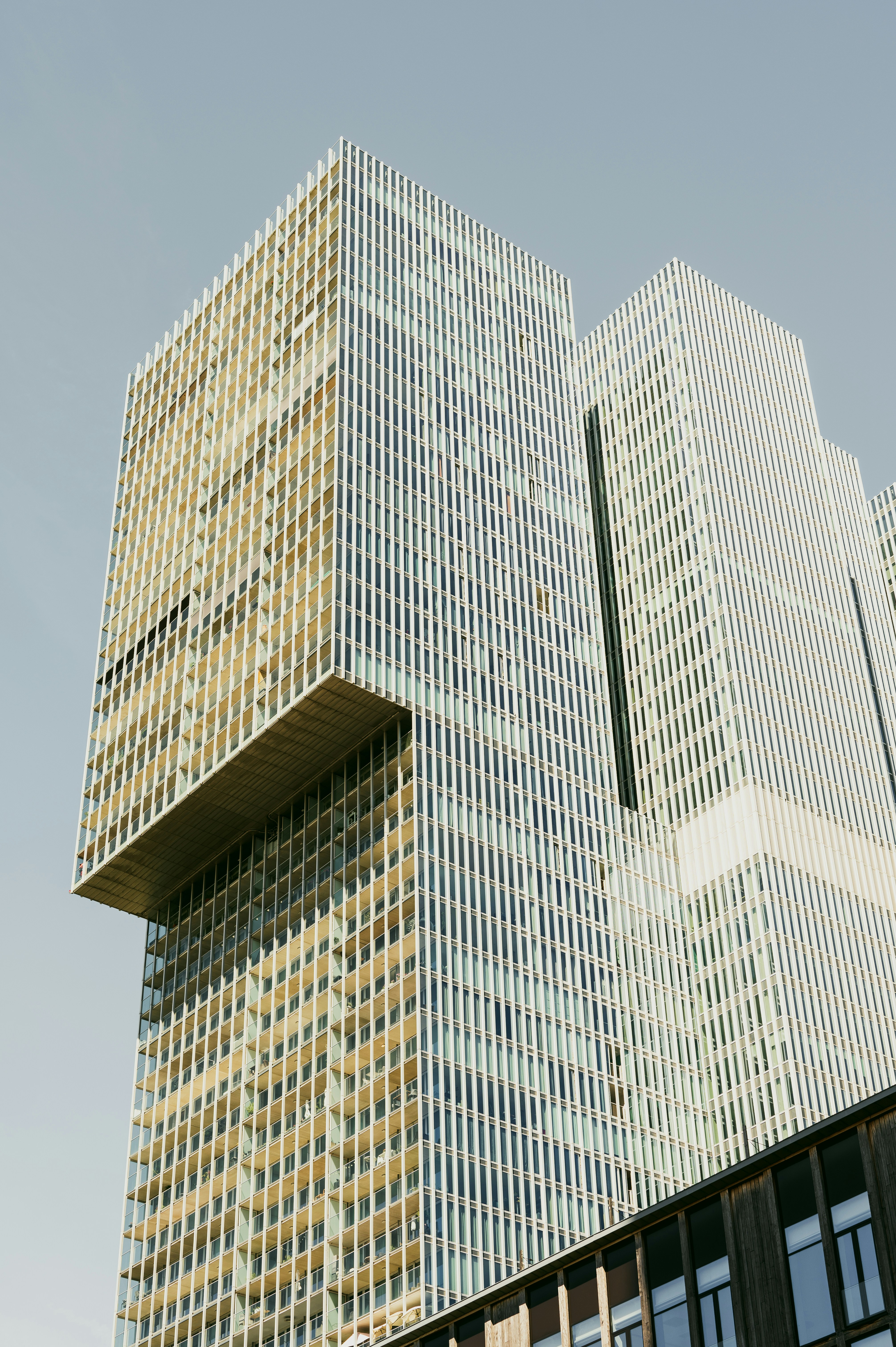 Perspective view of a modern glass skyscraper with offset, stacked blocks, bathed in daylight. The architecture emphasizes modular design and geometric rhythm.